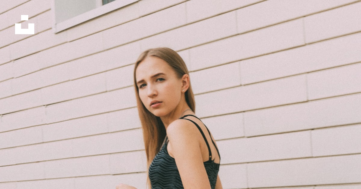 Woman In Black Tank Top And Blue Denim Jeans Standing Beside White Wall