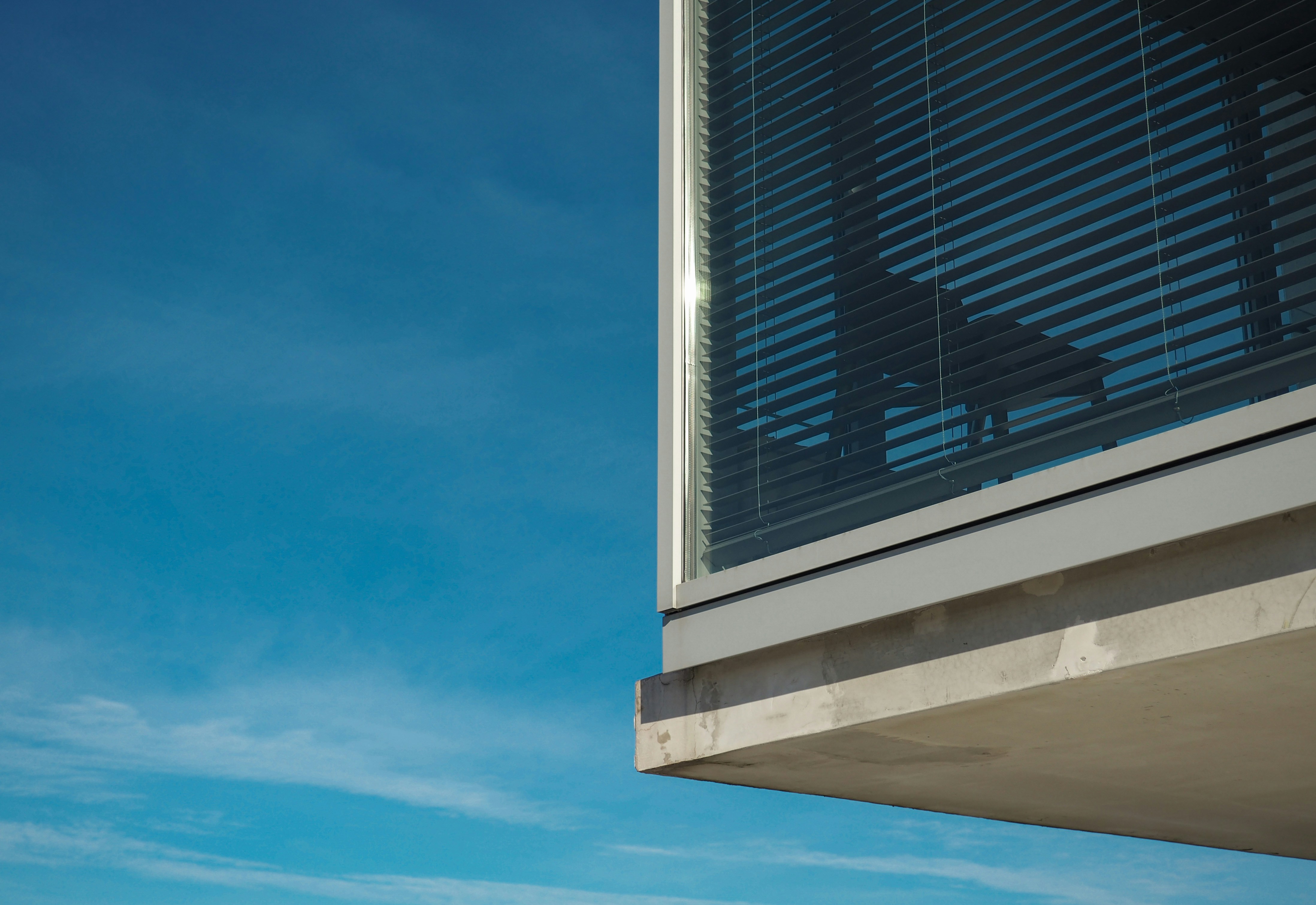 Corner of a modern building with sleek lines and glass panels set against a vibrant blue sky.