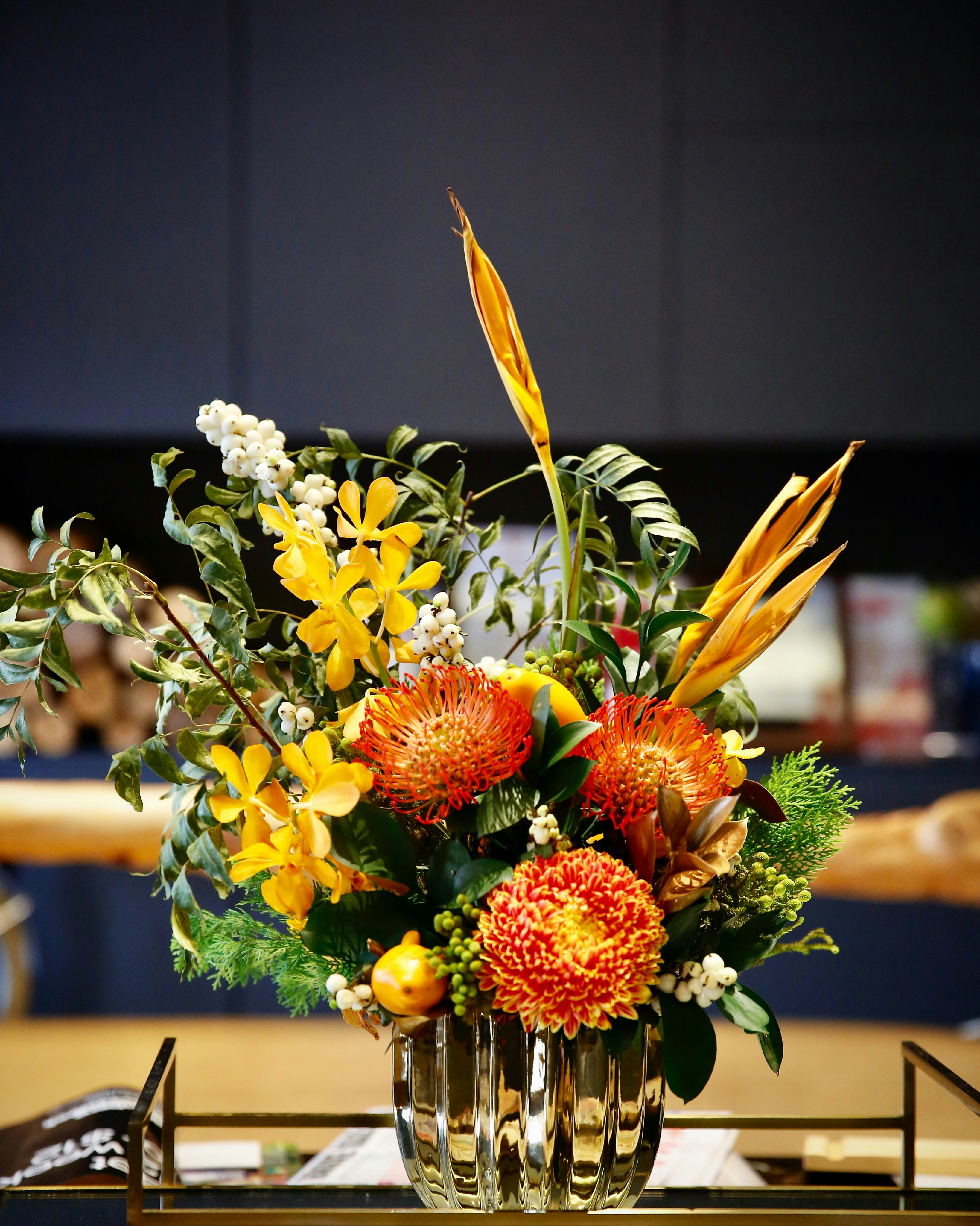 A beautifully arranged bouquet featuring bright orange and yellow flowers, complemented by lush greenery in a glass vase.