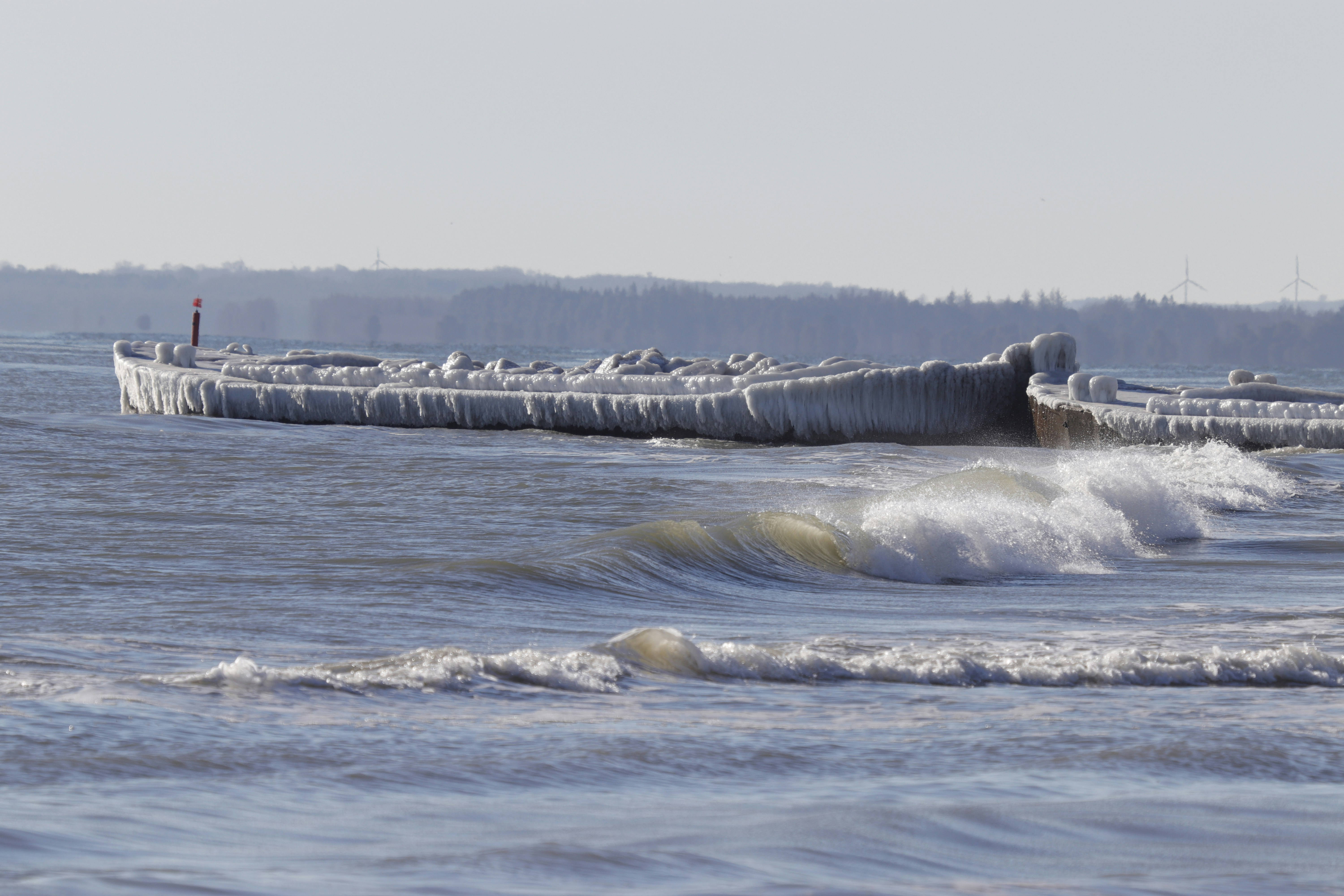 Ice-Coated Breakwaters Meet Quiet Waves Under a Pale Sky