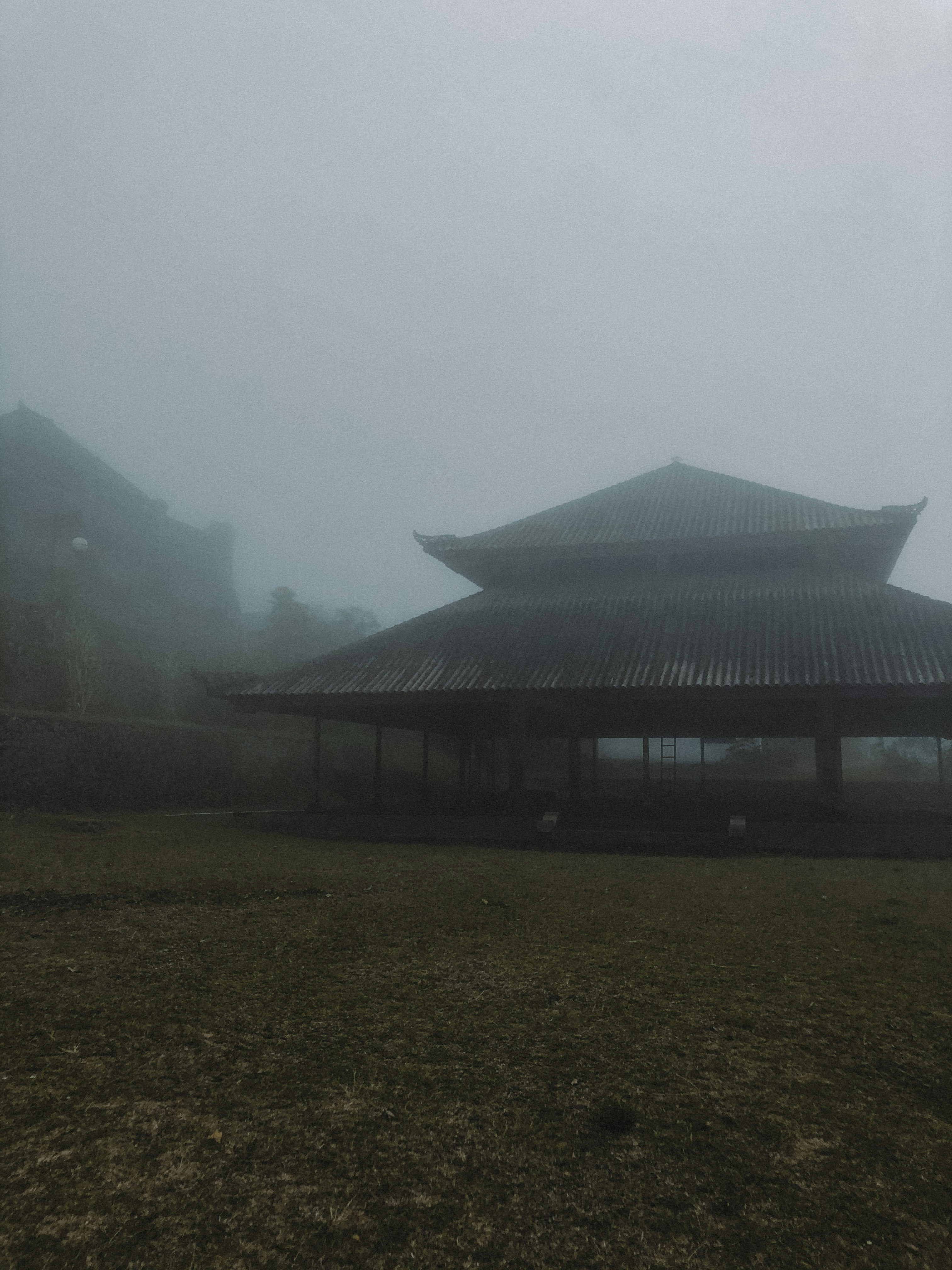 Mysterious traditional structure shrouded in fog, surrounded by lush greenery. The atmosphere evokes a sense of tranquility and contemplation.
