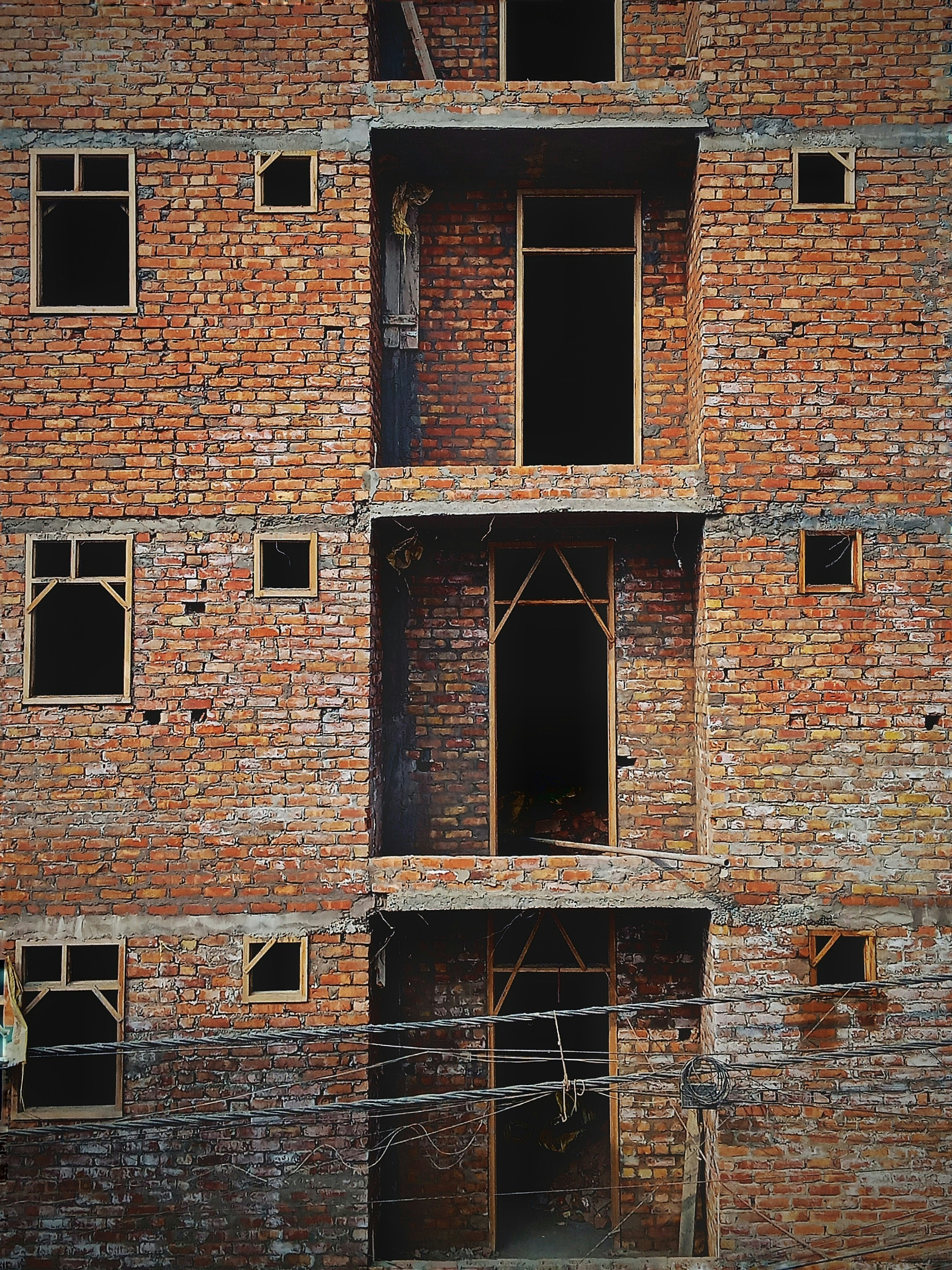 Exposed brick facade of a multi-story building under construction, showcasing empty windows and unfinished spaces.