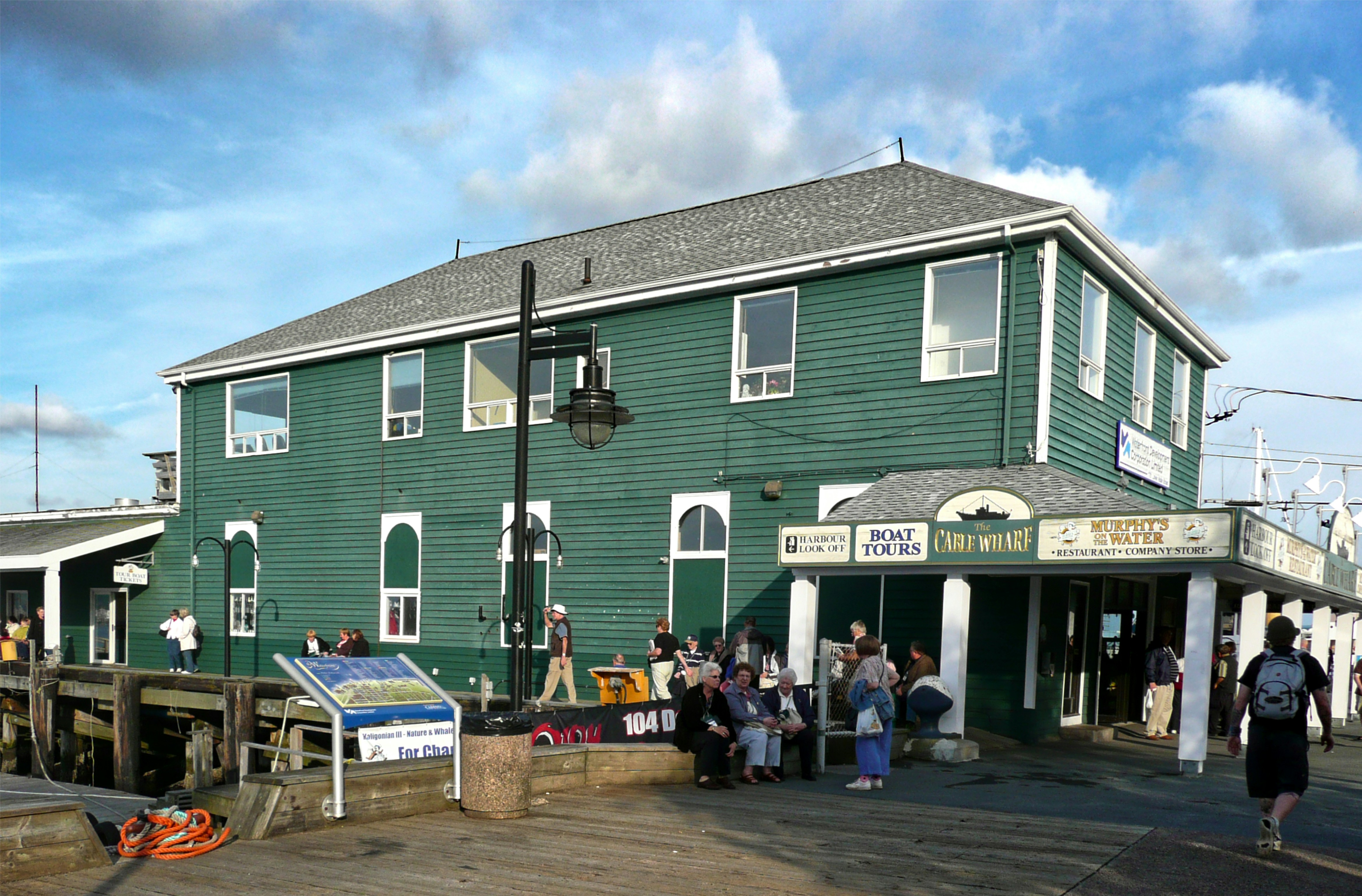 Green building housing boat tour services with people gathered outside on a busy pier.