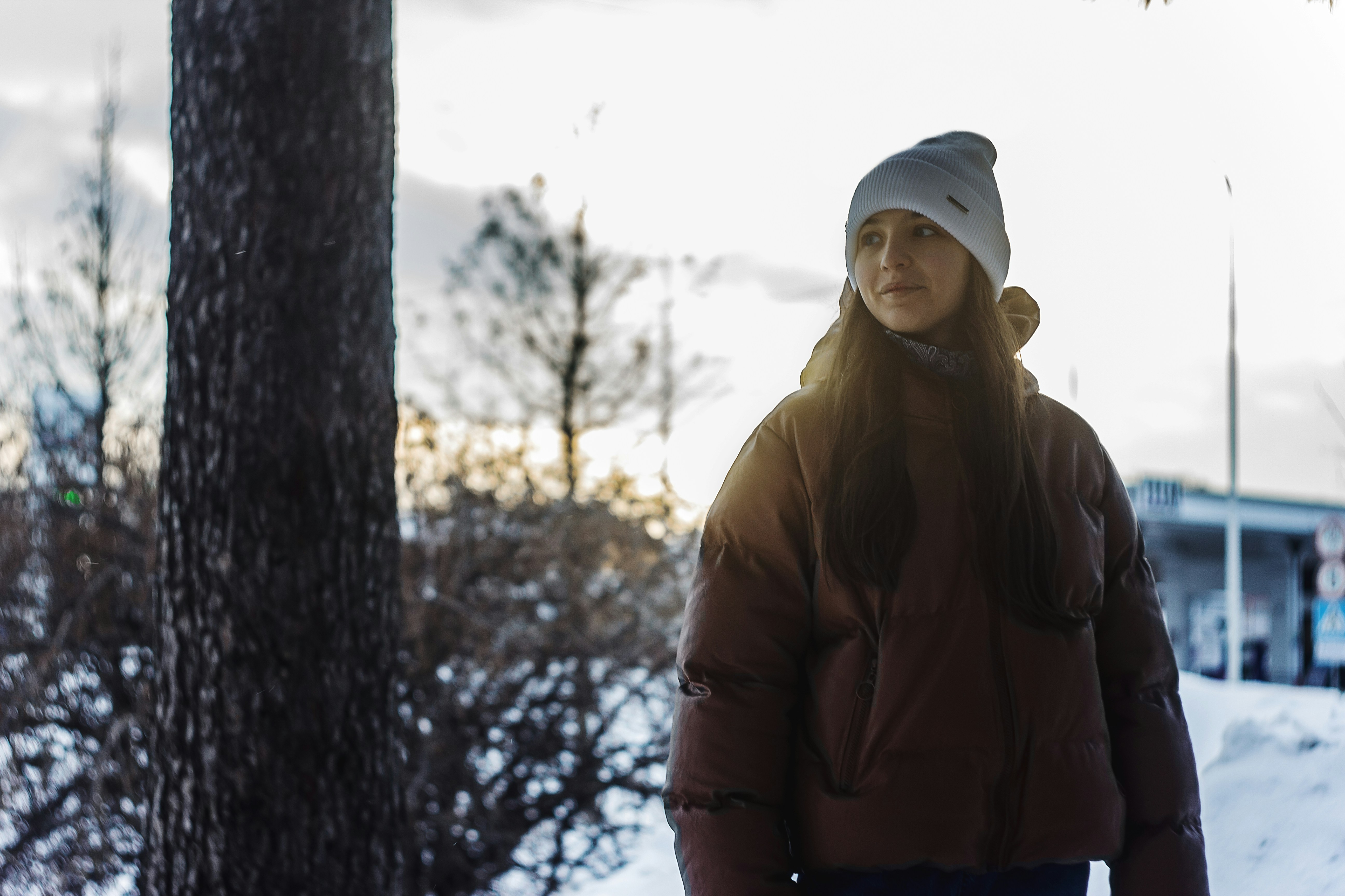 woman in brown jacket and white knit cap standing near brown tree during daytime
