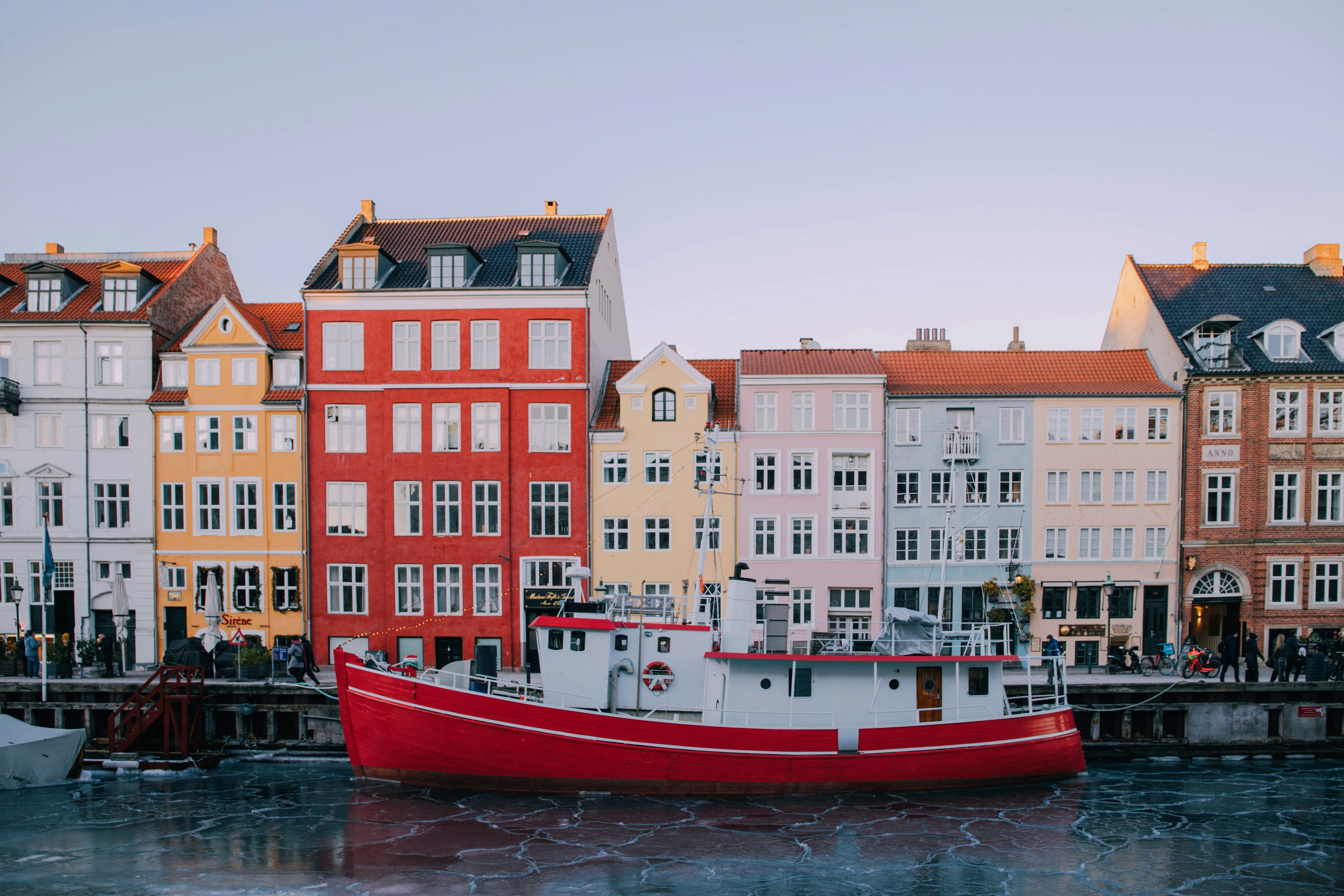 Red and white boat moored in icy water against a backdrop of colorful buildings.