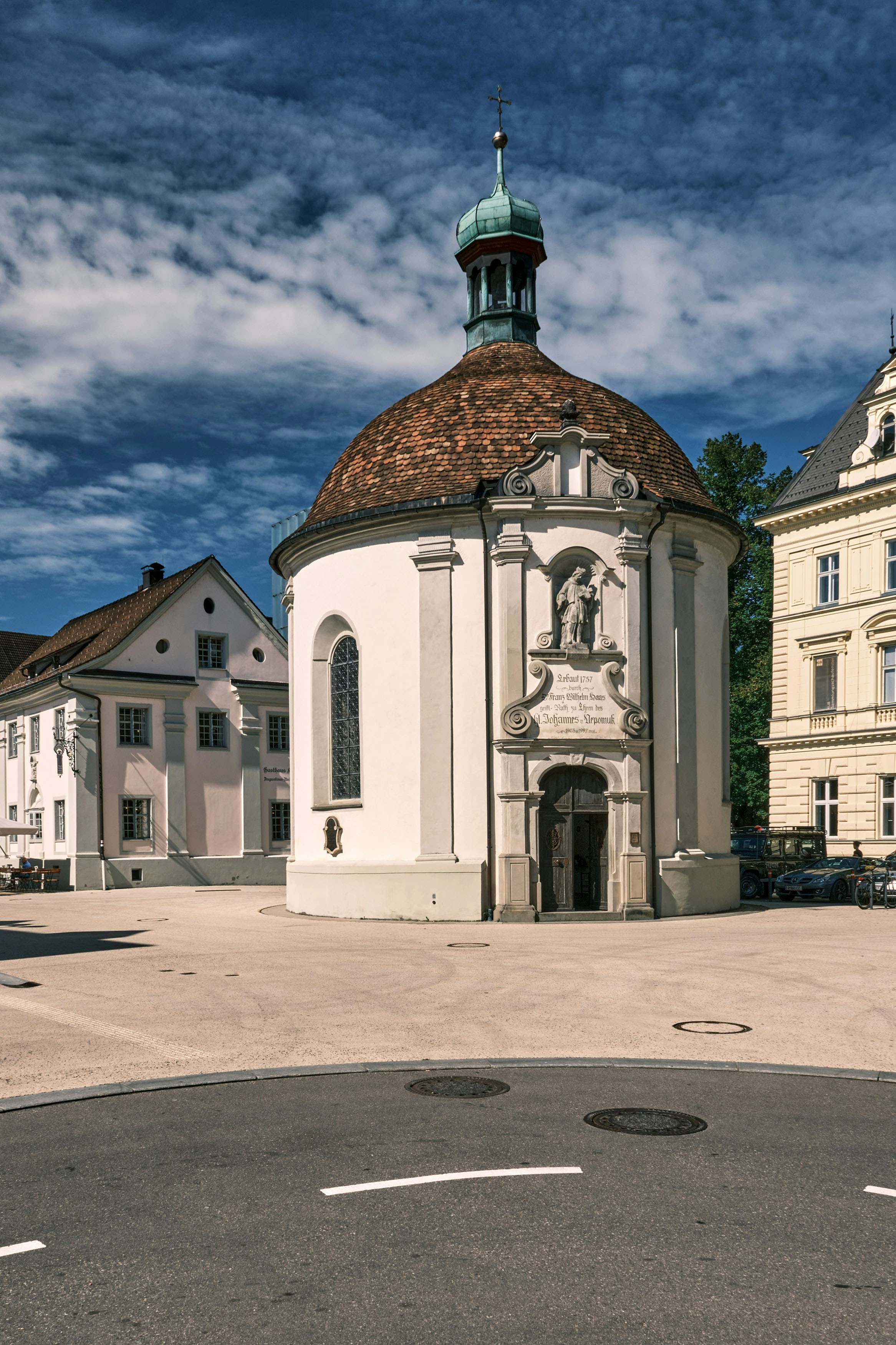 A charming circular chapel with a distinct domed roof, surrounded by elegant buildings and a clear blue sky.