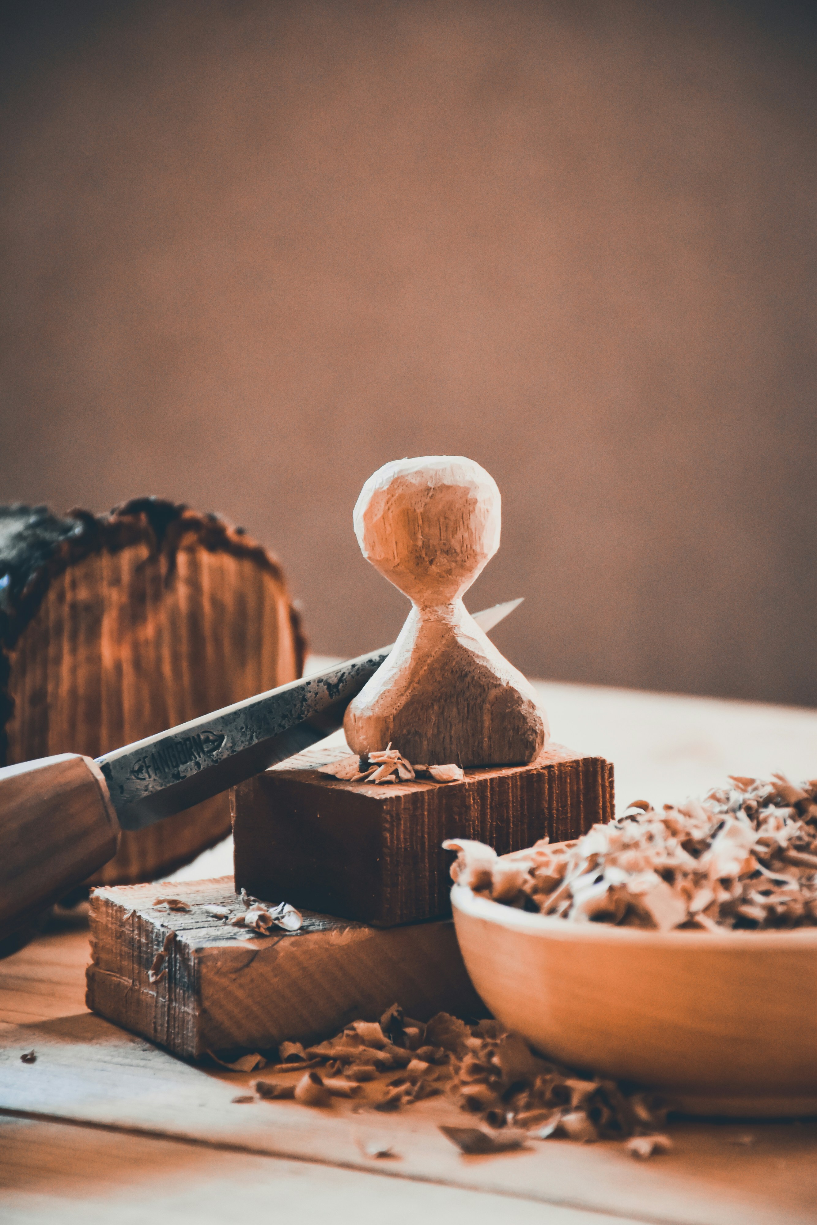 A wooden figure in the midst of creation, surrounded by shavings and tools on a workbench.