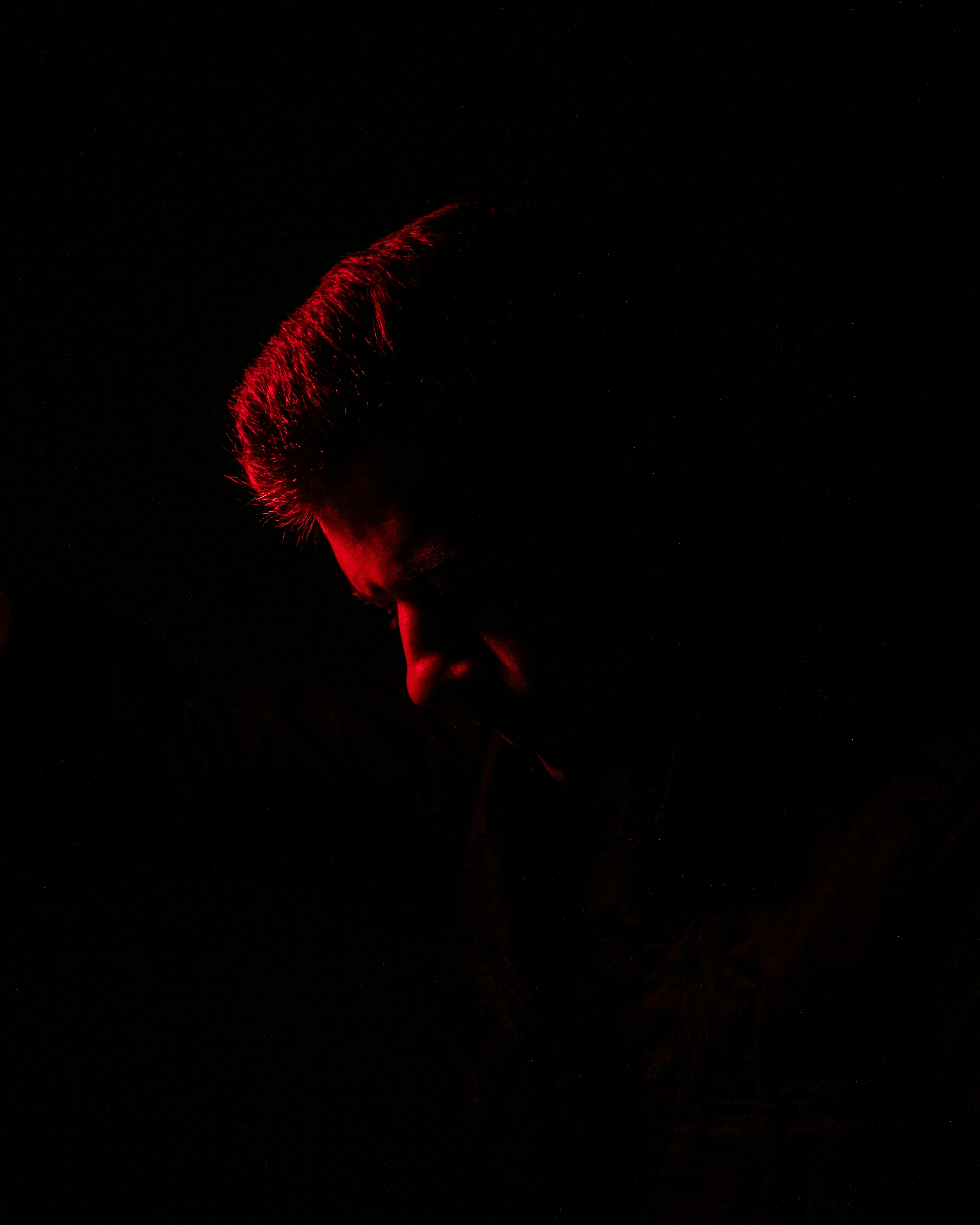 Silhouette of a person against a dark background illuminated by a striking red light, highlighting the contours of their face and hair.