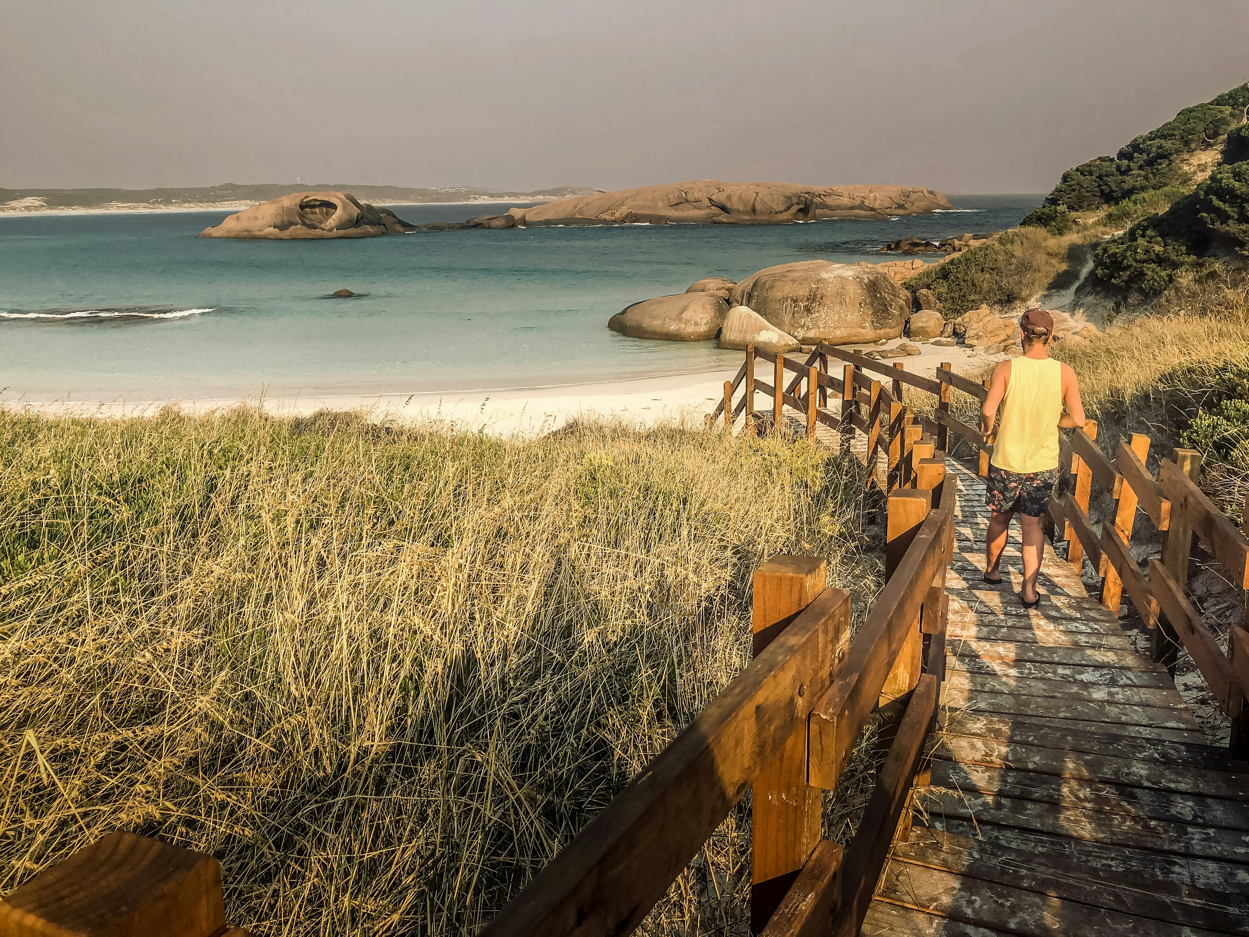 Hiker on a Weathered Coastal Boardwalk Toward Turquoise Waters