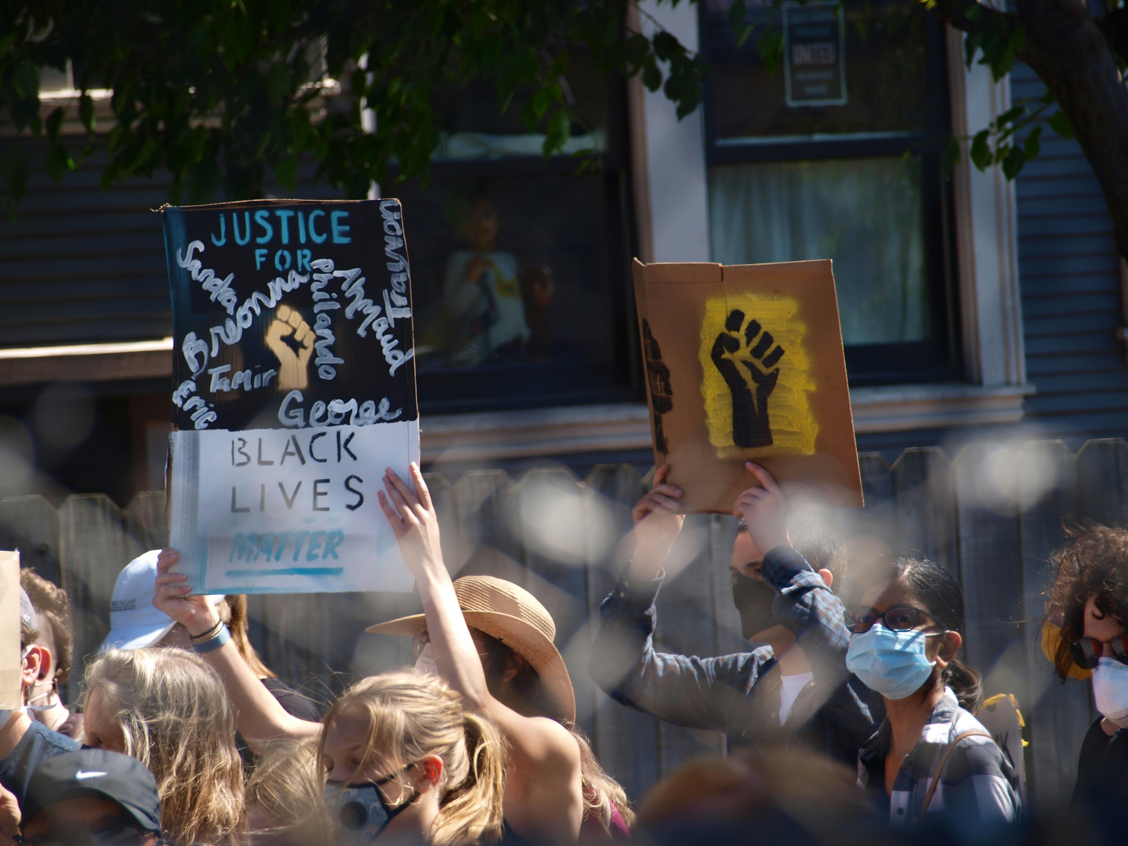 Protesters hold signs advocating for justice and equality in a sunny urban setting.