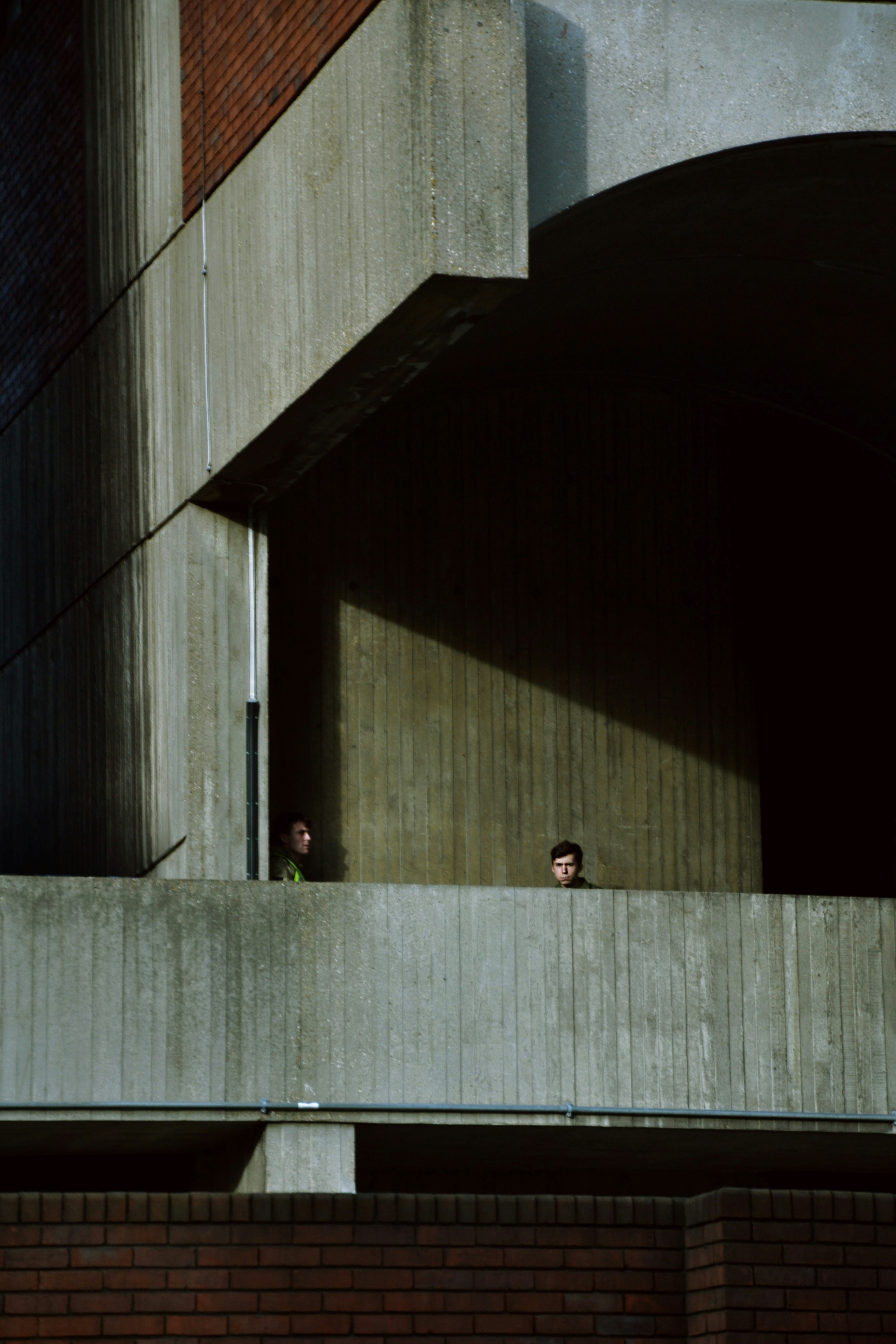 Two Observers on a Weathered Concrete Balcony Beneath a Looming Arch