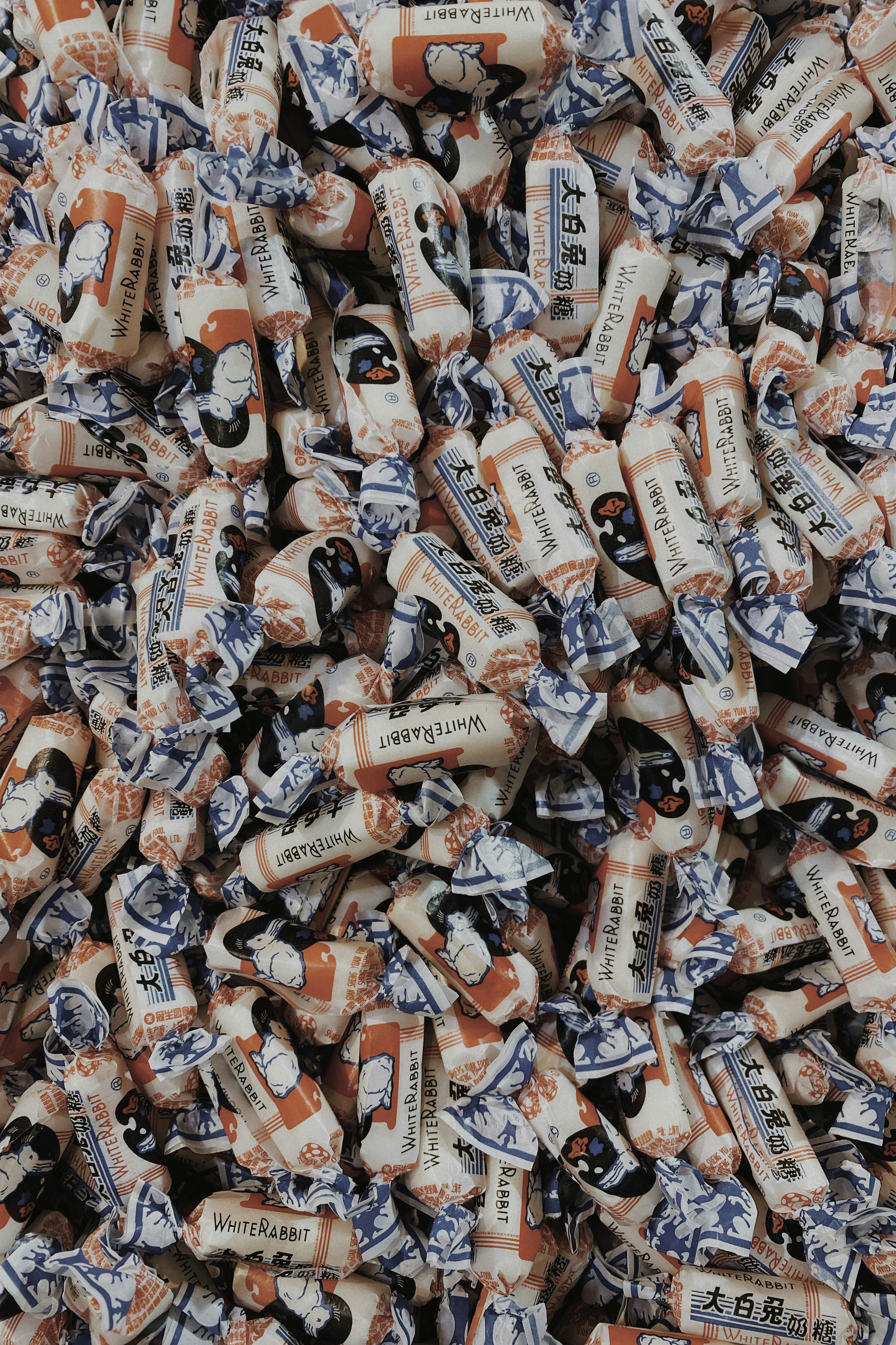A dense pile of White Rabbit candy wrappers in orange and blue, highlighting the brand's rabbit illustration.