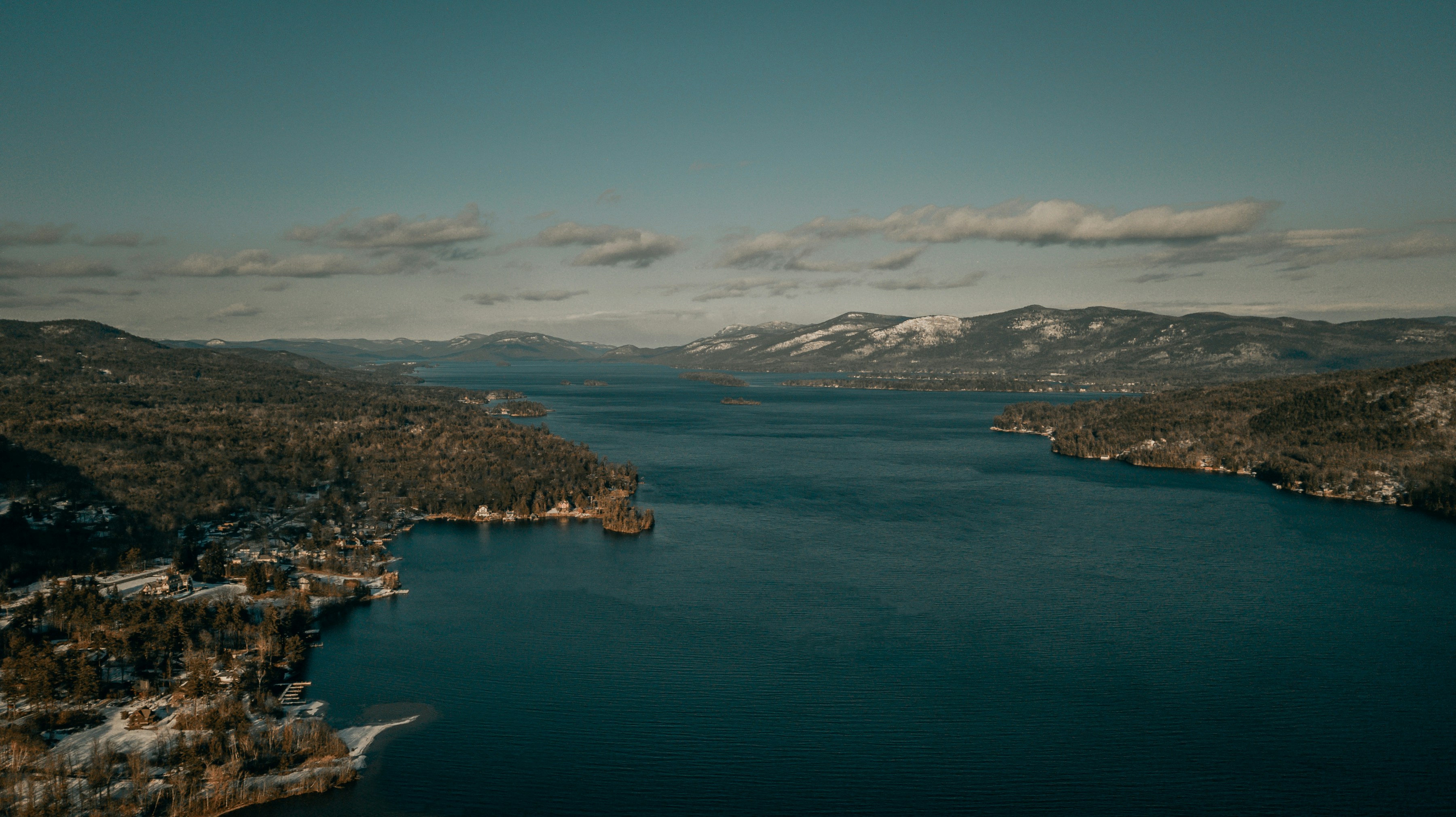 Expansive view of Lake George with surrounding forested hills under a clear sky.