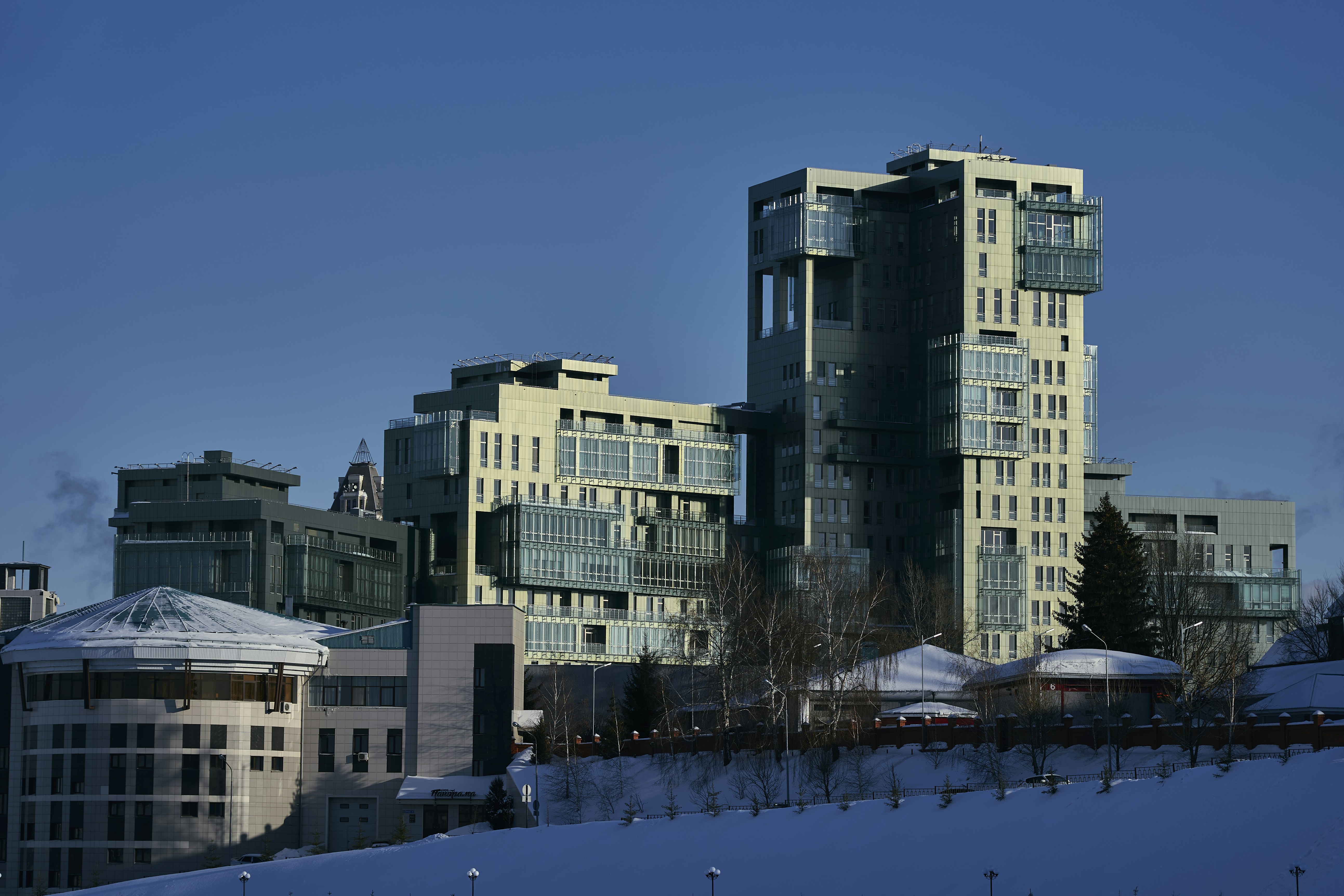 A cluster of contemporary buildings showcasing unique geometric designs, illuminated by the soft winter sun against a clear blue sky.