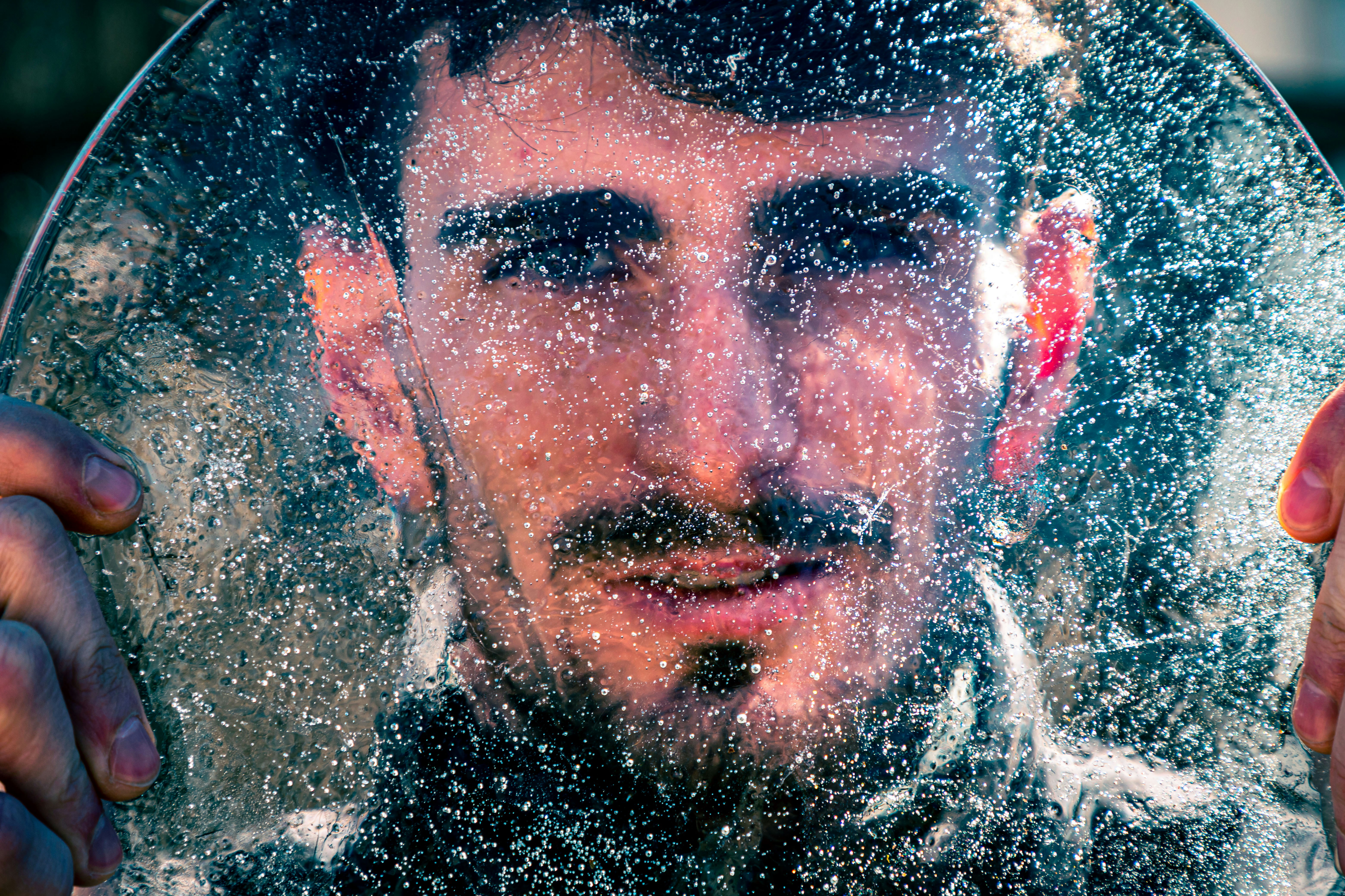 A young man holds a reflective surface, capturing his determined expression amidst a backdrop of sparkling frost.