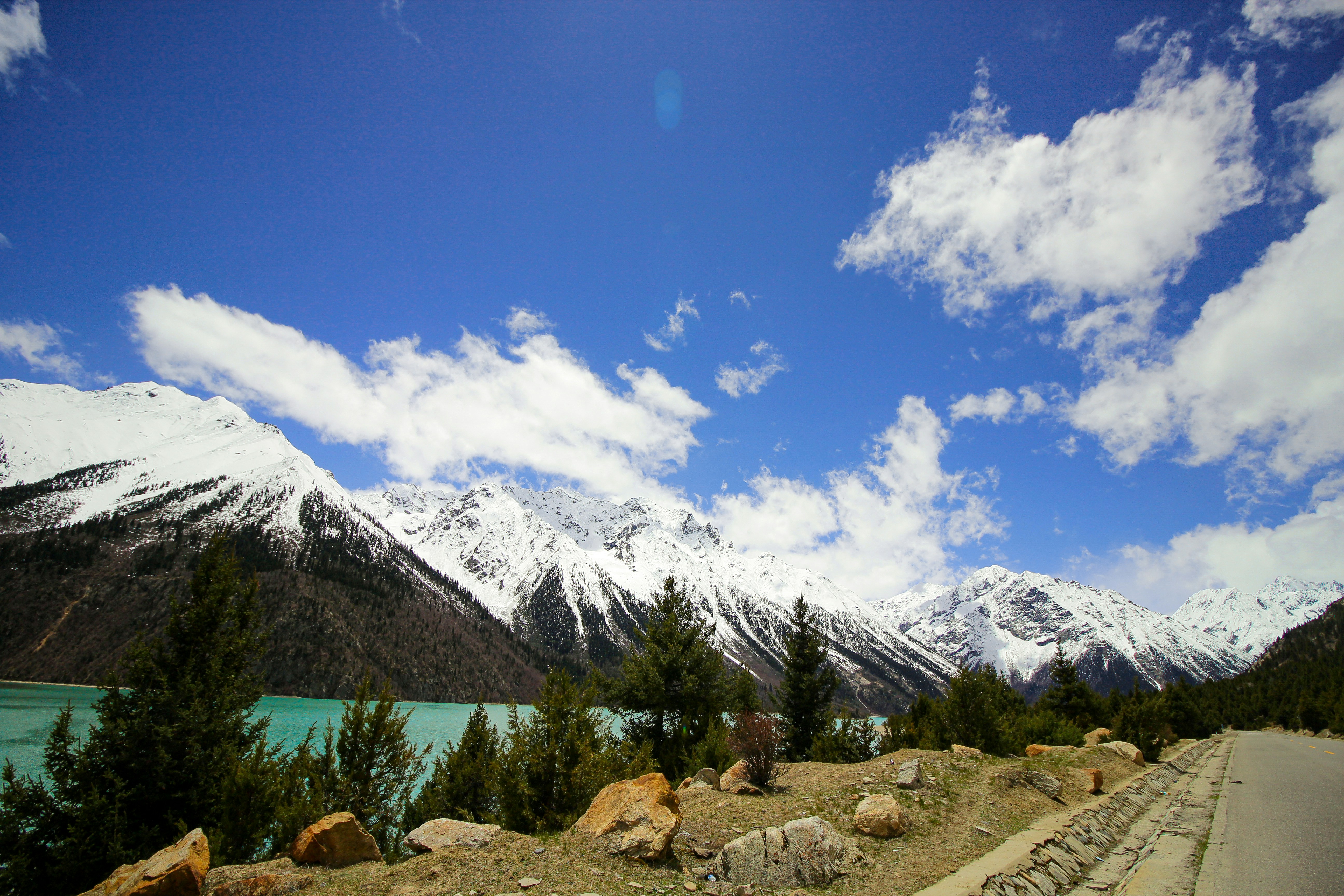 Snow-covered mountains under a bright blue sky with green trees by a turquoise lake.