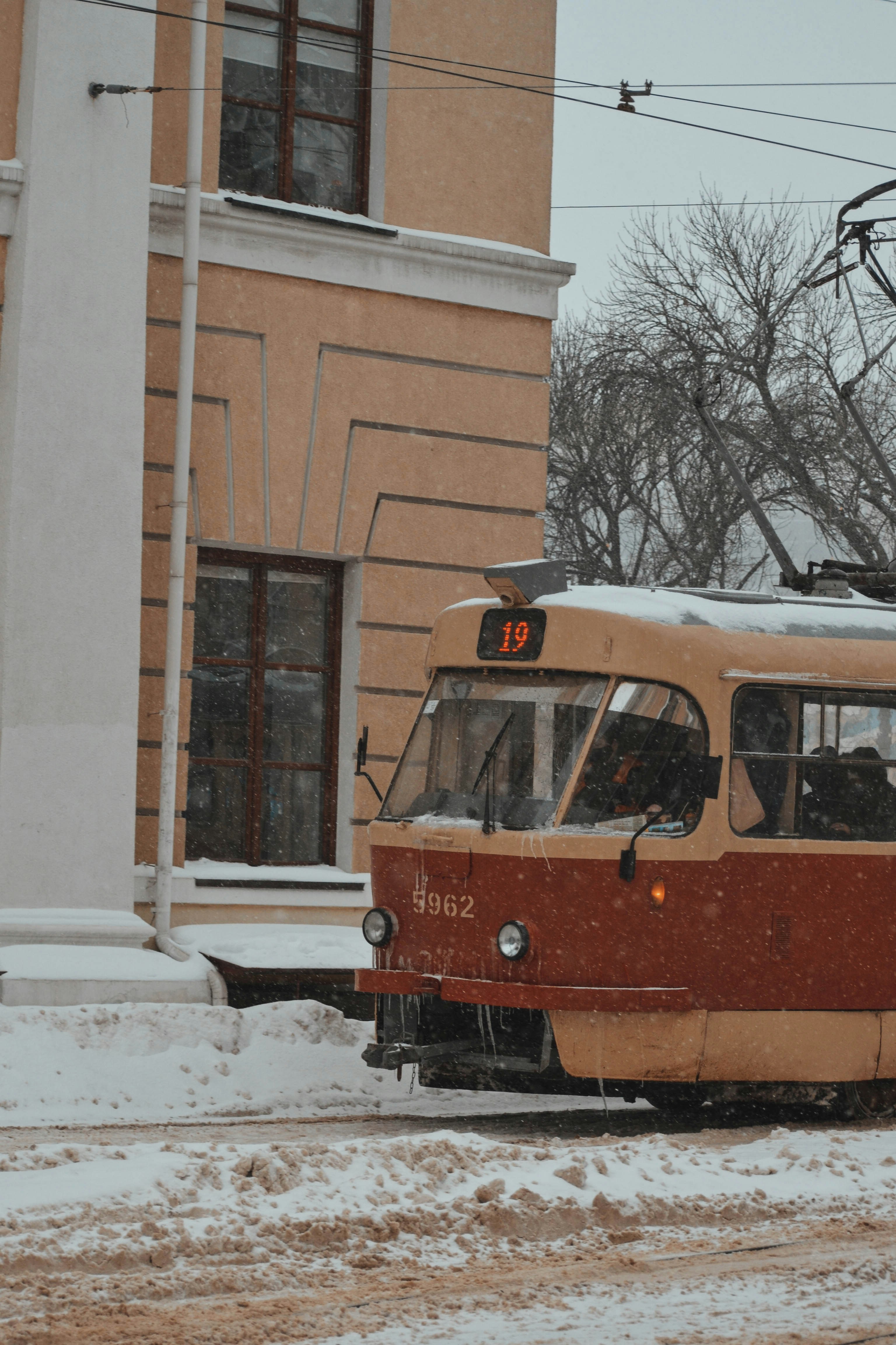 A vintage tram navigating through a snowy urban landscape, with a visible route number displayed. The scene captures the charm of winter transportation.
