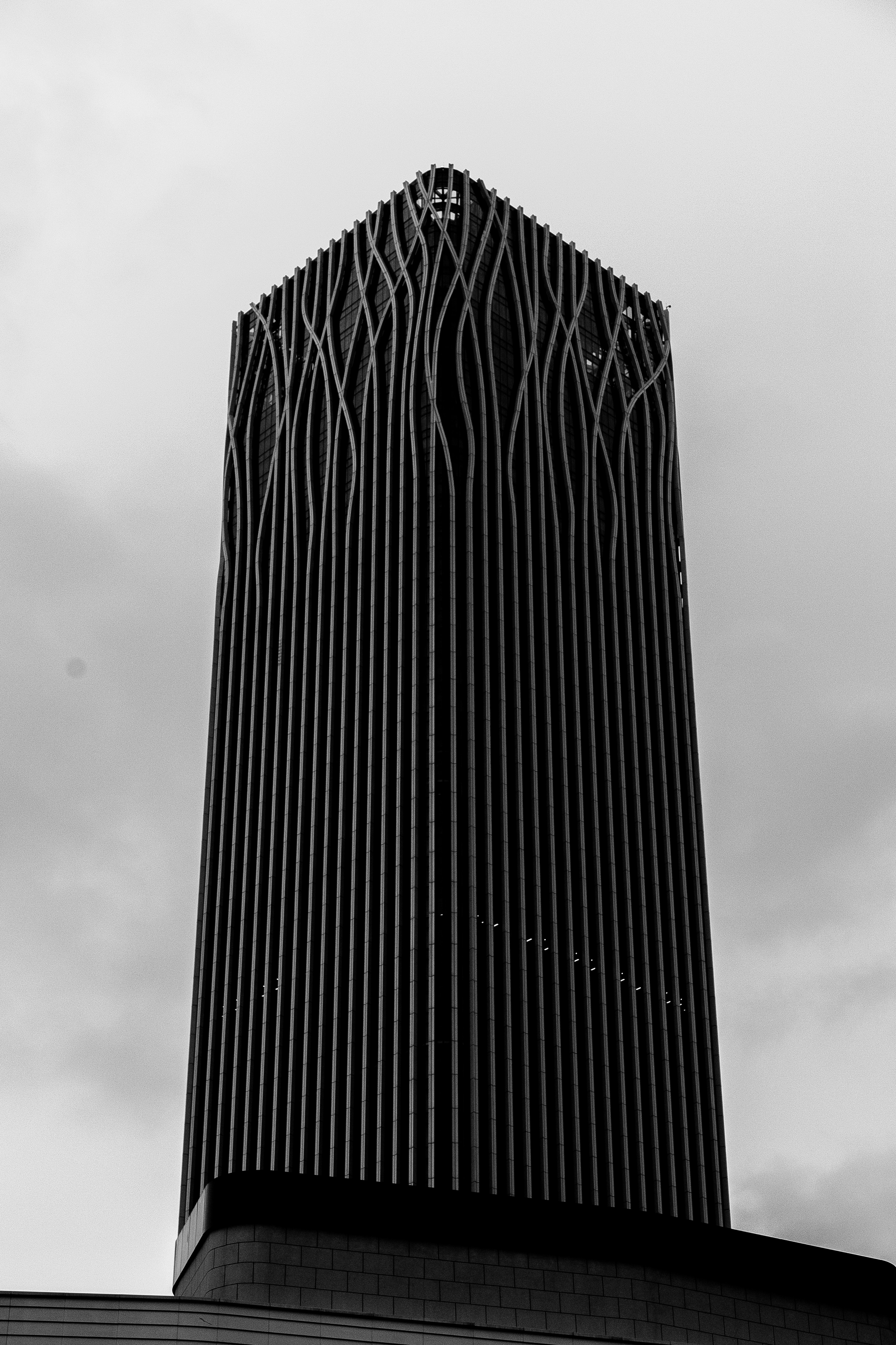 A striking black and white depiction of a modern skyscraper, showcasing its unique wave-like façade against a cloudy sky.
