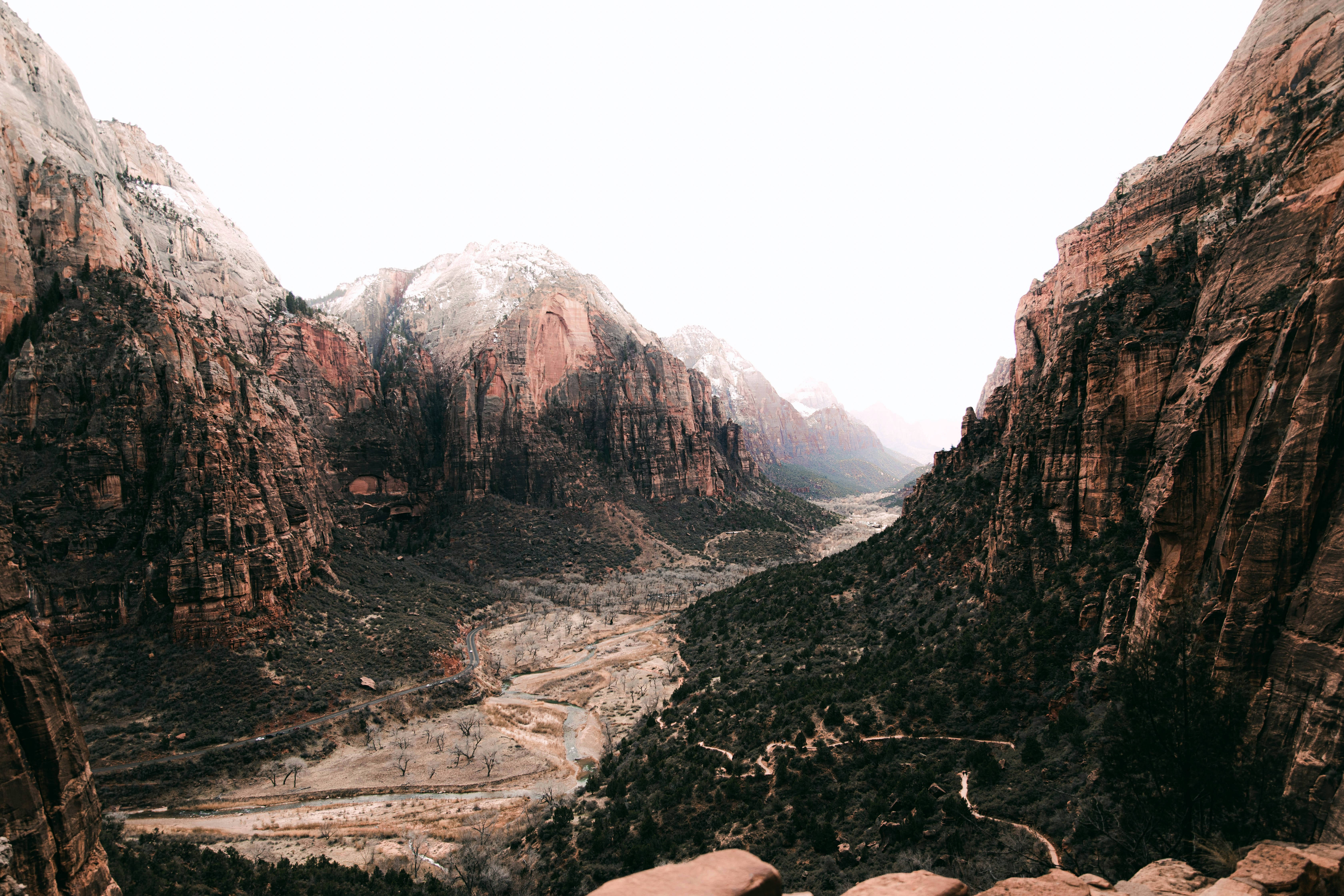 Expansive canyon landscape with rugged cliffs and a winding valley beneath a bright white sky.
