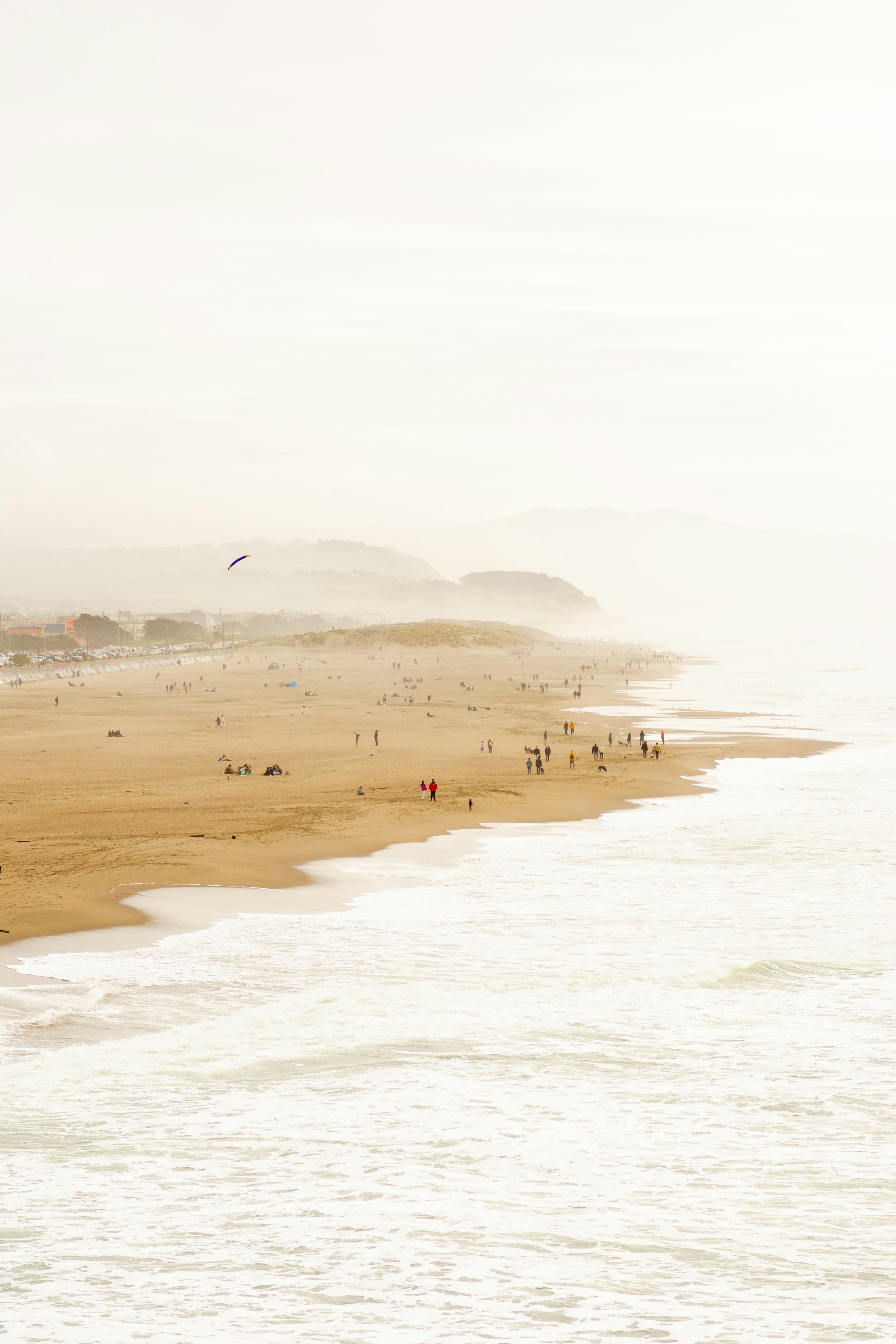 People stroll along Ocean Beach in San Francisco under a soft, golden mist.