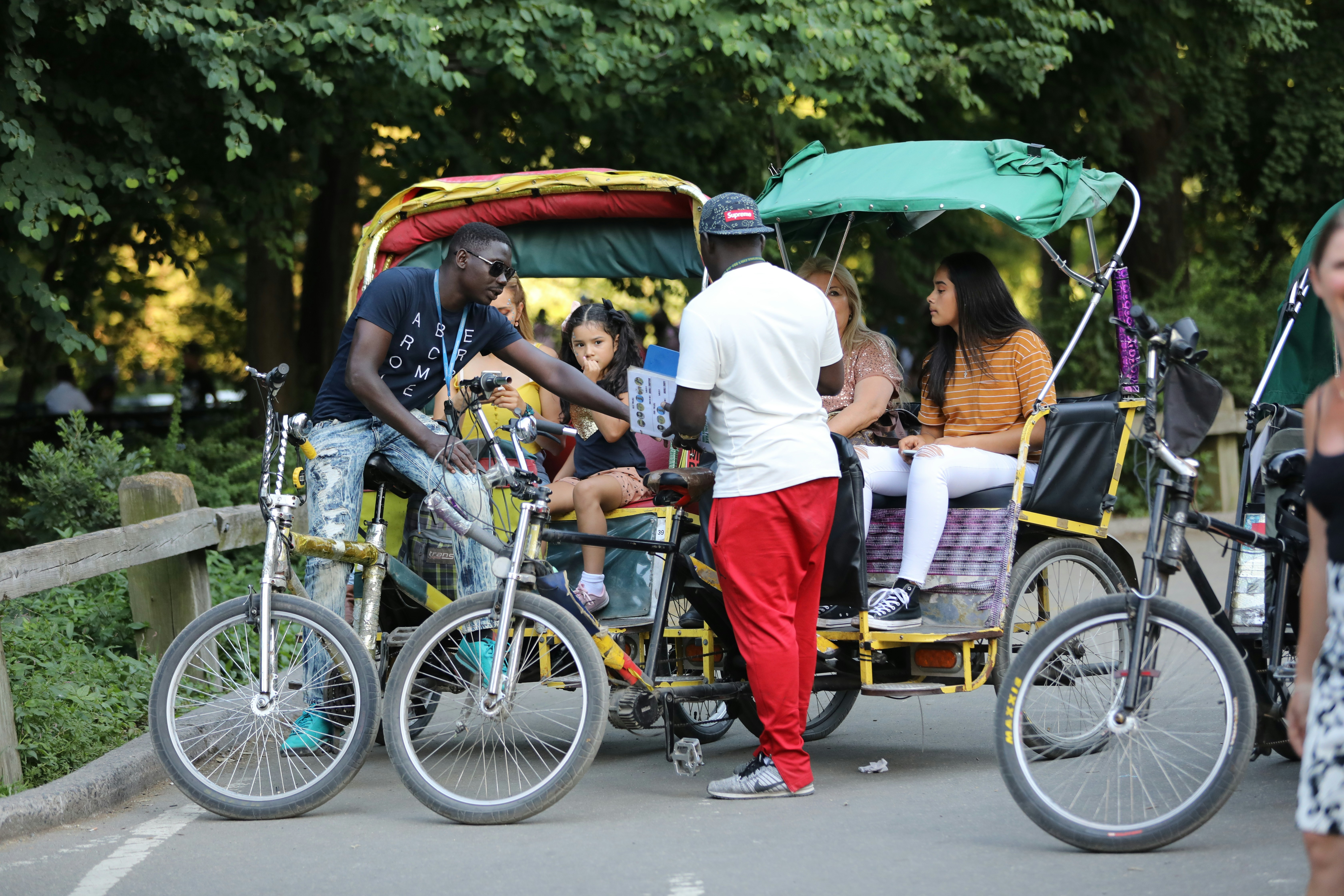 Conversations on Wheels: A Sunlit Pedicab Stop Amid Parkside Greenery