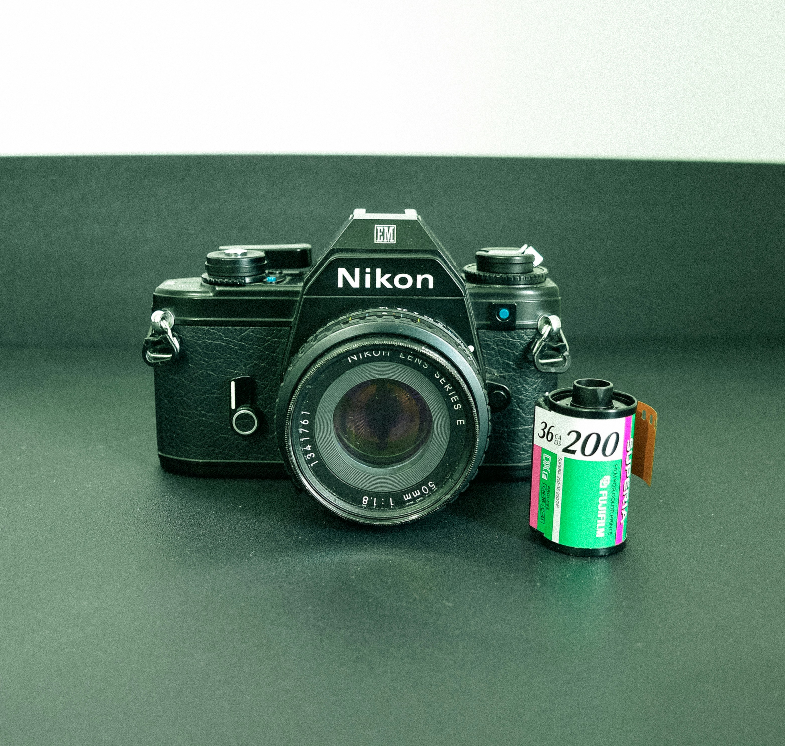 Classic Nikon camera model with a roll of film beside it, set against a minimalist black background.