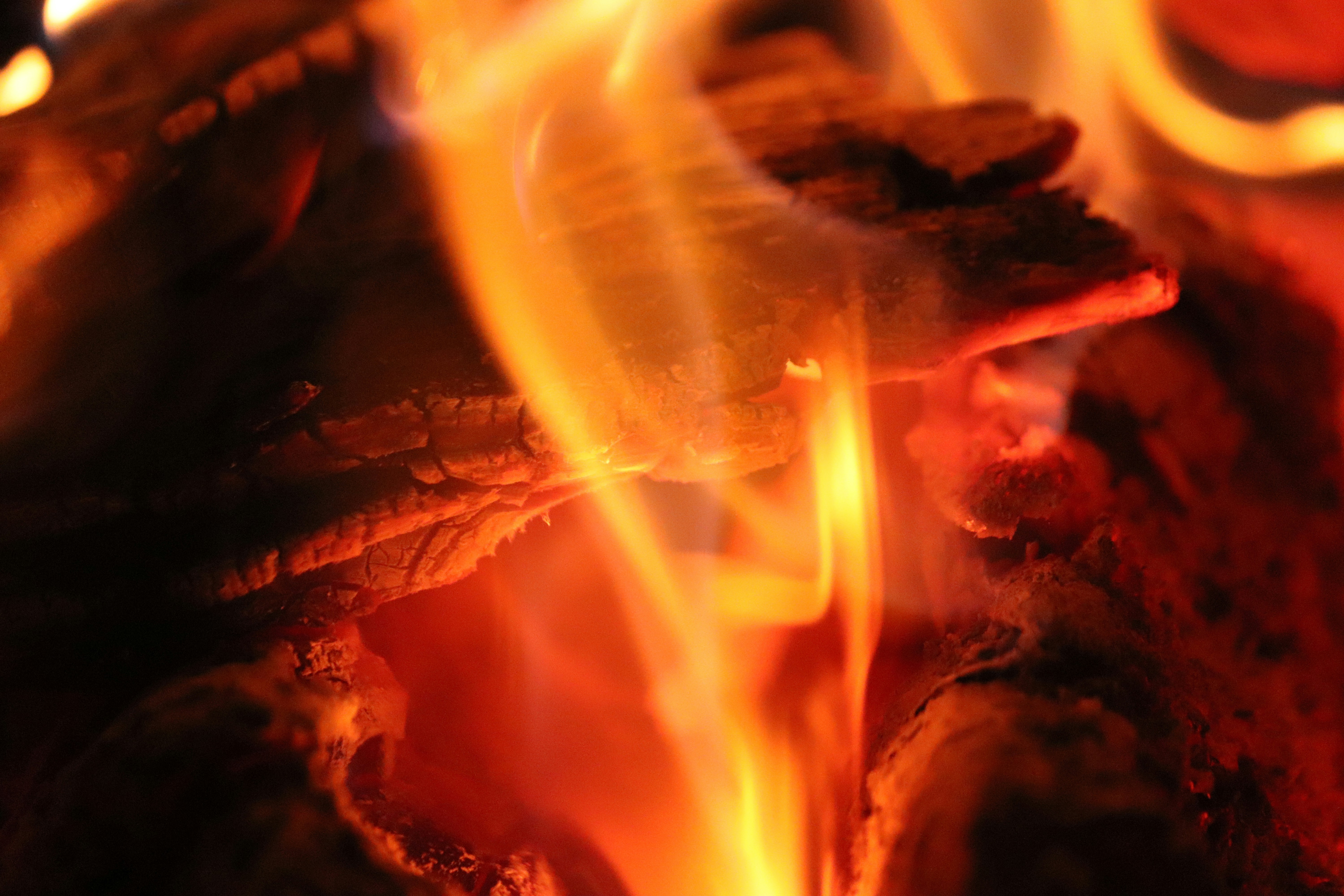 Close-up of glowing embers and flickering flames, showcasing the intricate textures of burning wood. The vibrant colors create a mesmerizing visual experience.