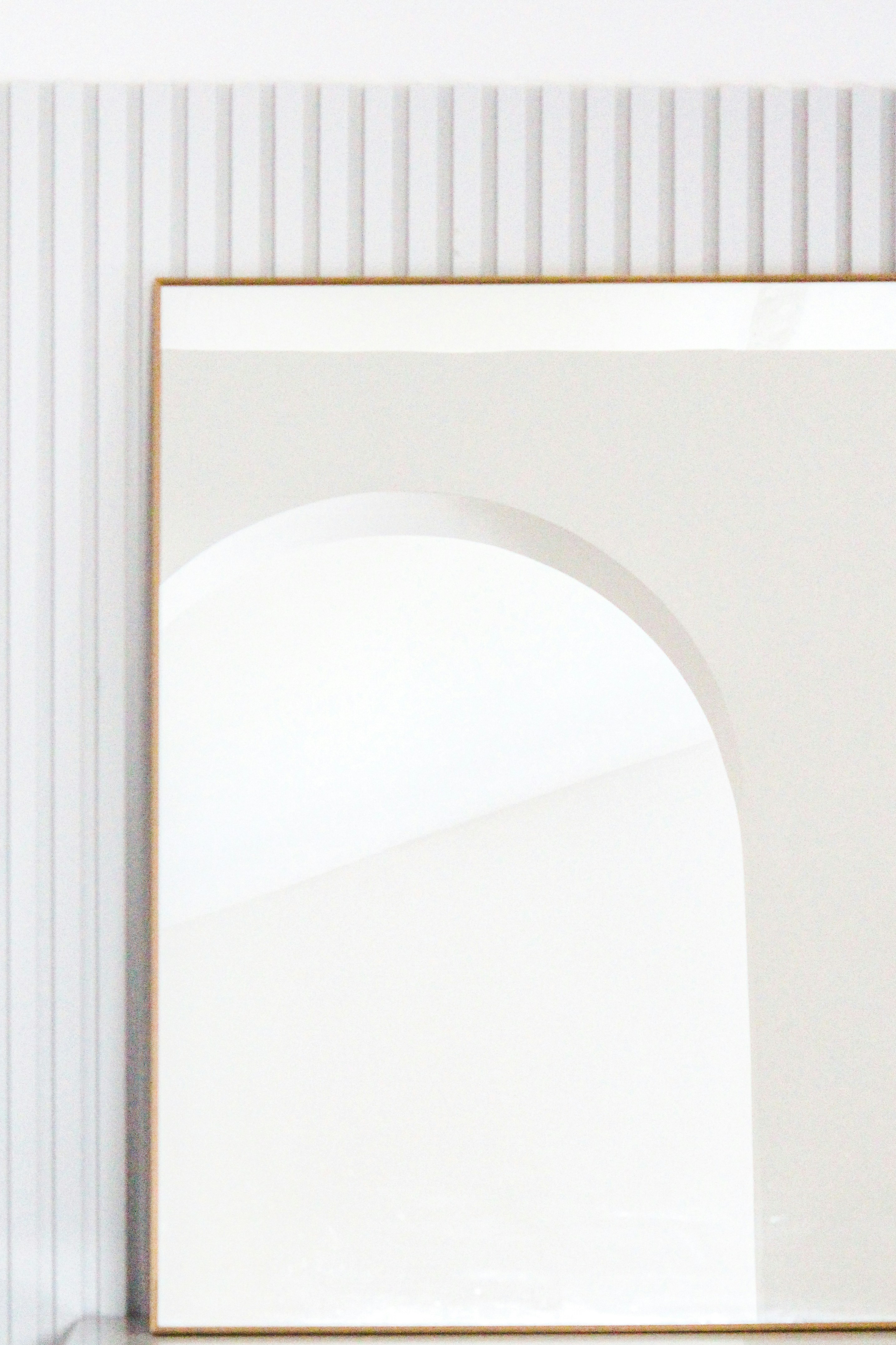 Minimalist interior with a wooden-framed mirror reflecting a soft arch against a striped wall.