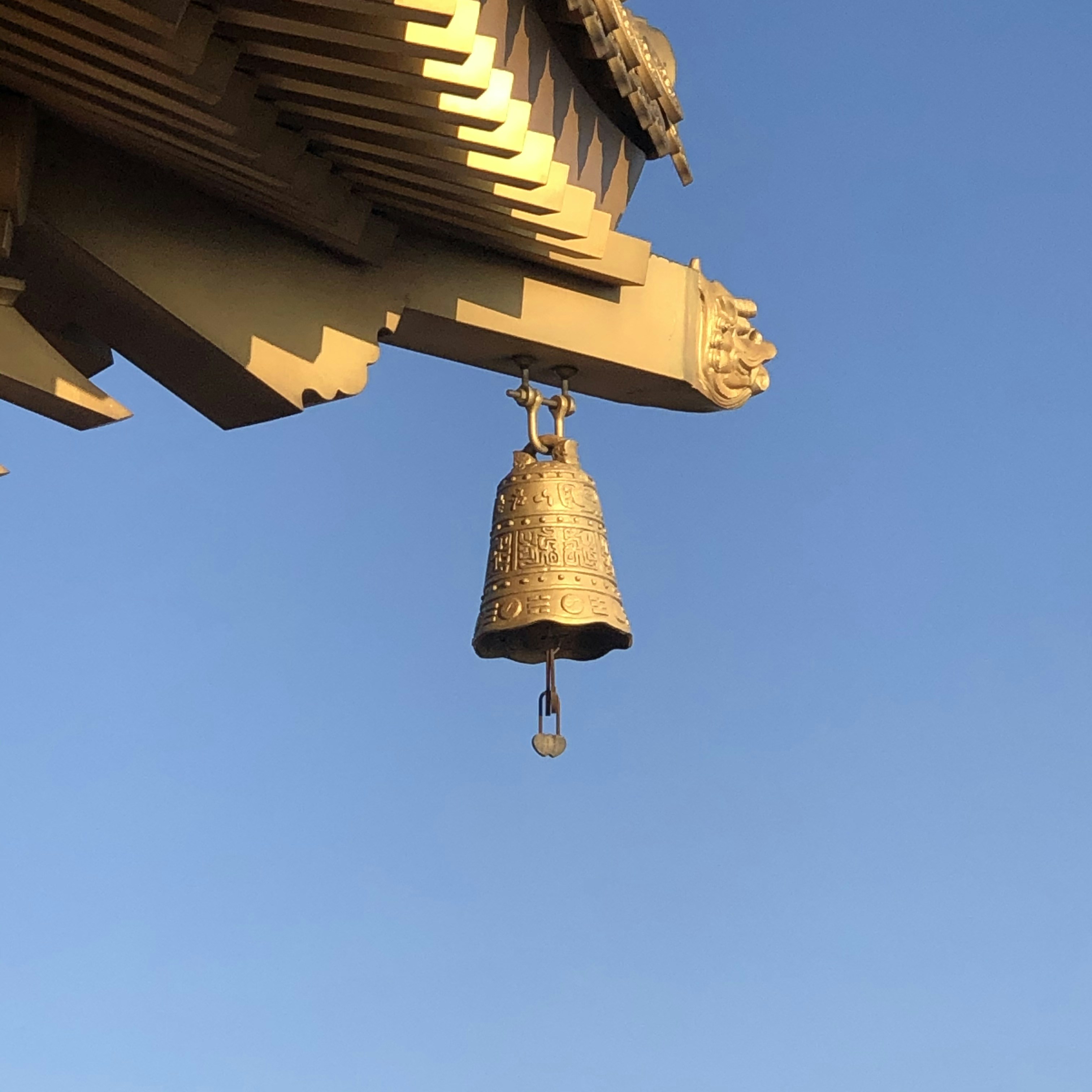 Golden bell suspended from an ornate structure against a clear blue sky, symbolizing tranquility and cultural significance.