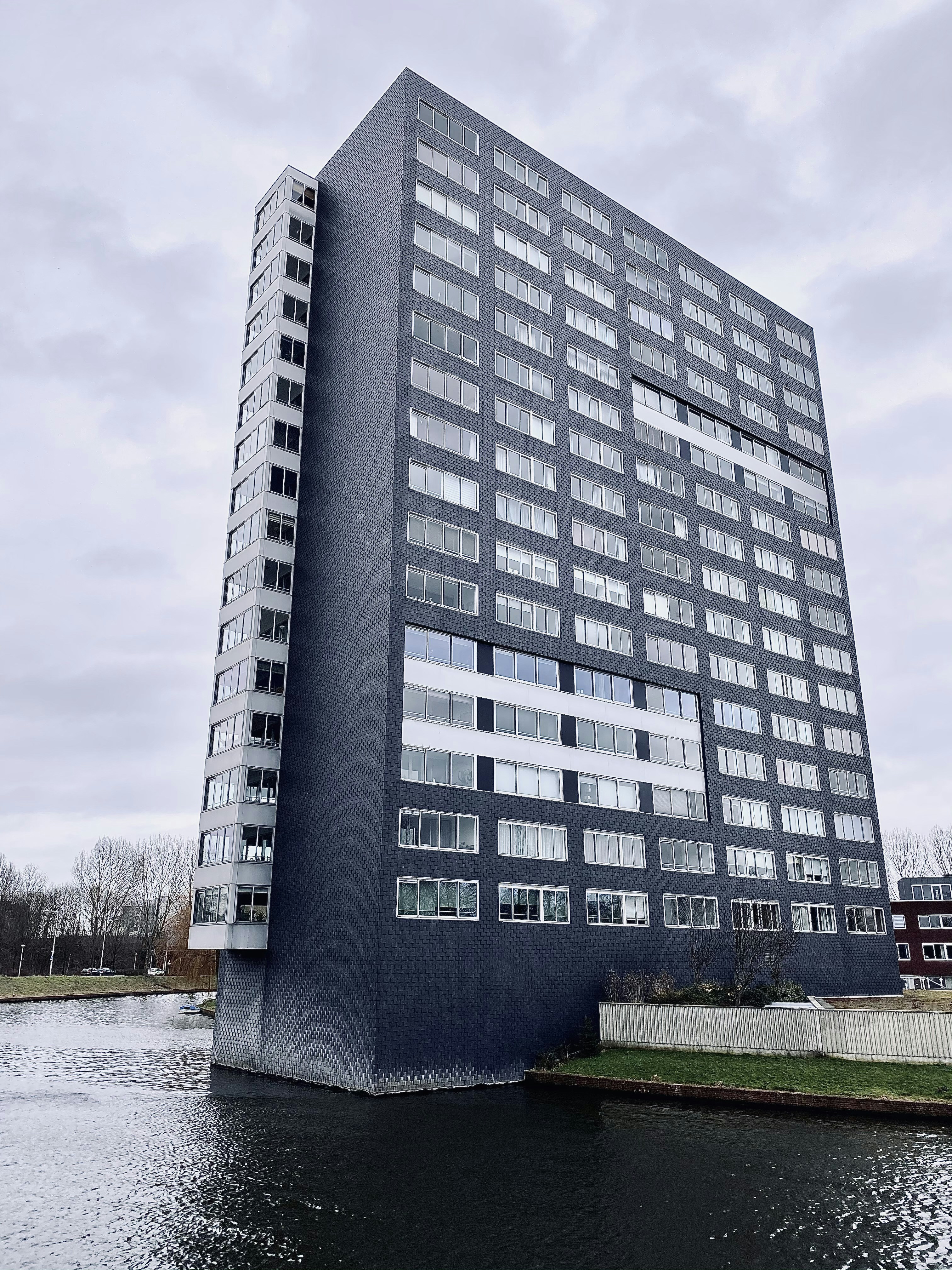 Canal-Side Monolith: A Dark High-Rise Crowned by Window Grids
