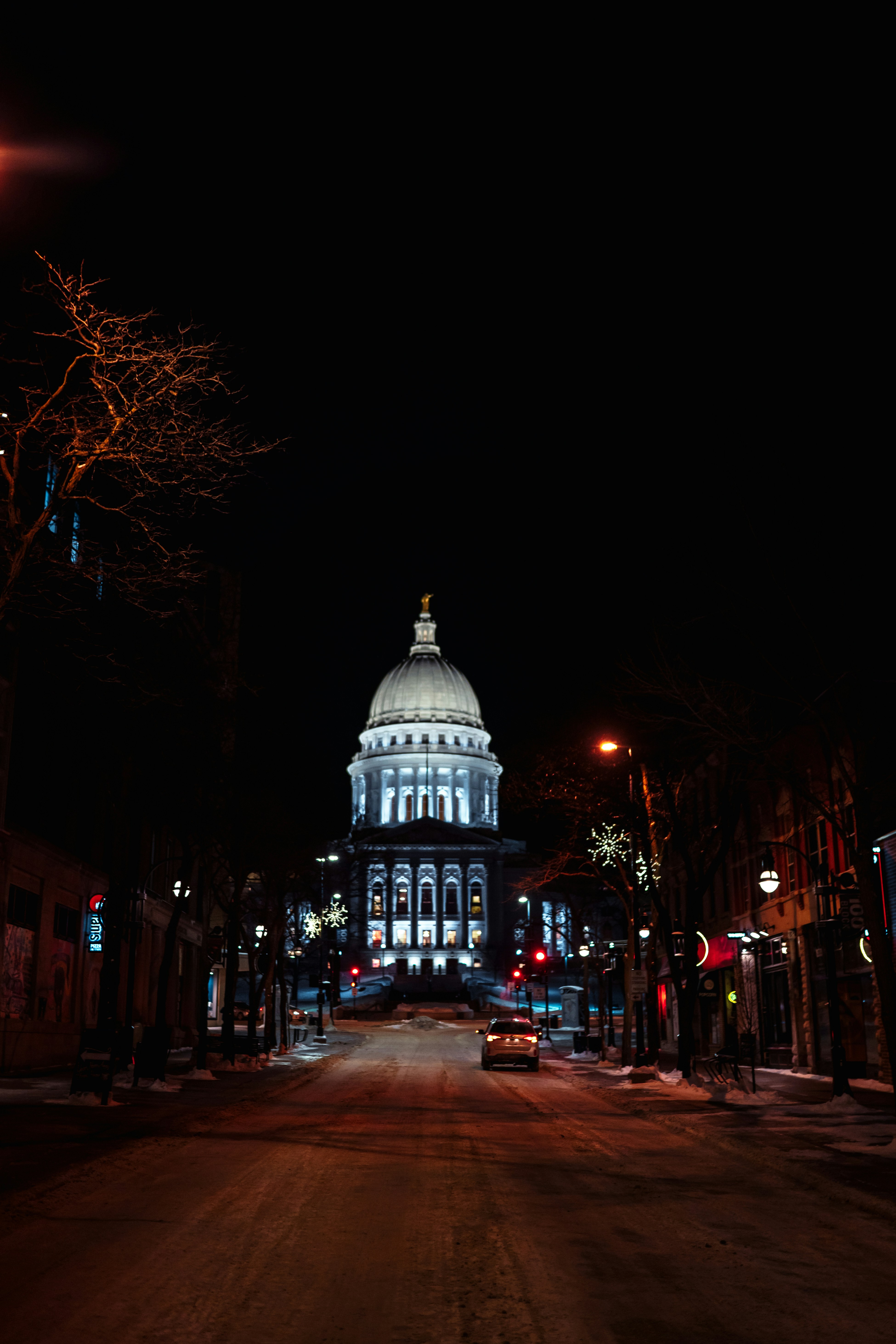 State Capitol building aglow with lights on a quiet winter night, surrounded by snow-covered streets and festive decorations.