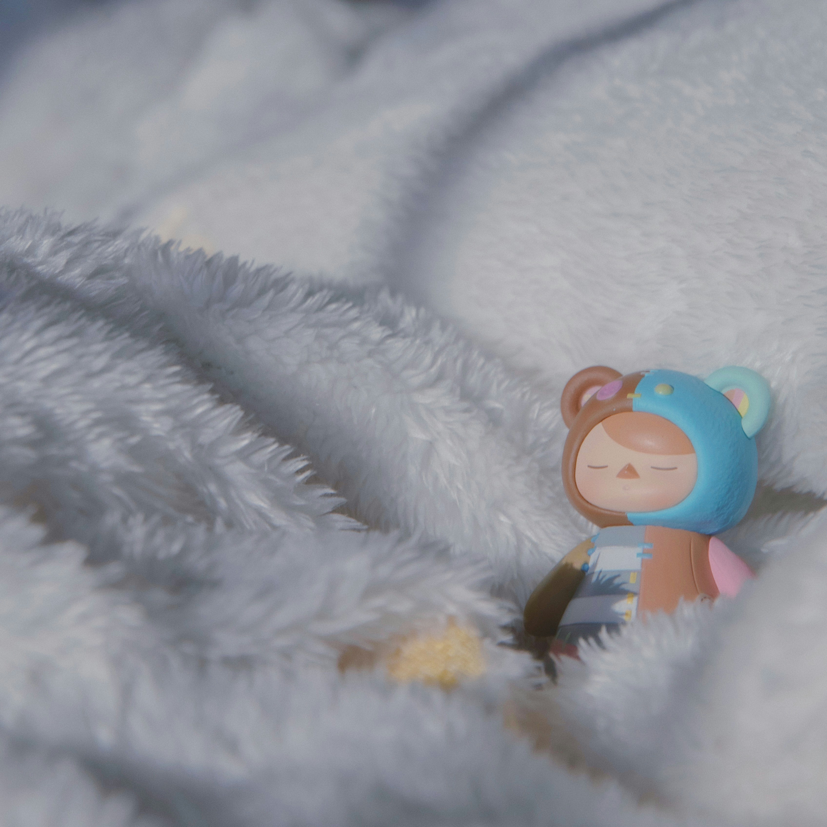 A cute figurine rests cozily among fluffy, textured fabric, inviting a sense of warmth and tranquility.