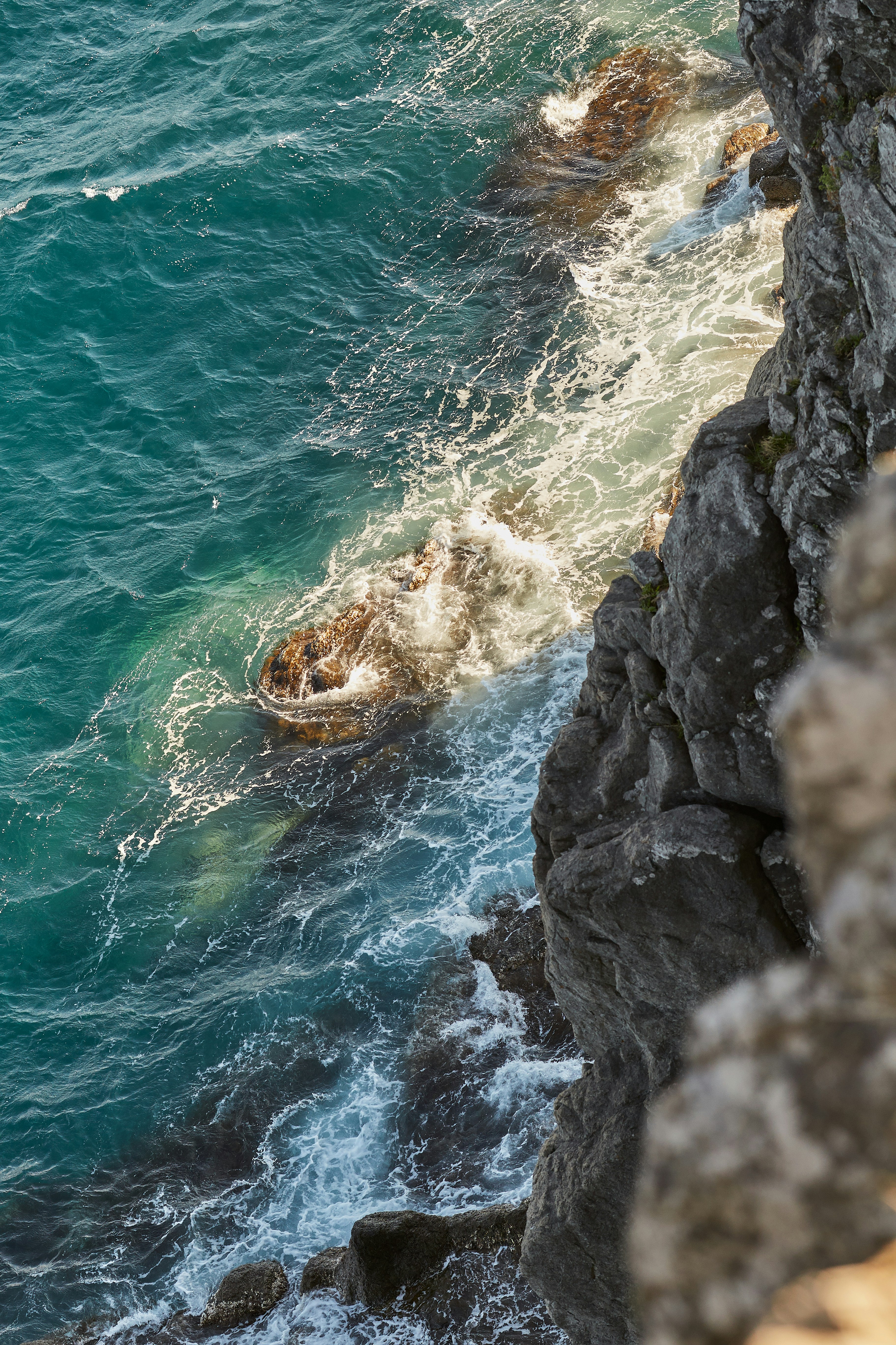 Turquoise Crest: A Circular Rock Framed by Cliffside Surf