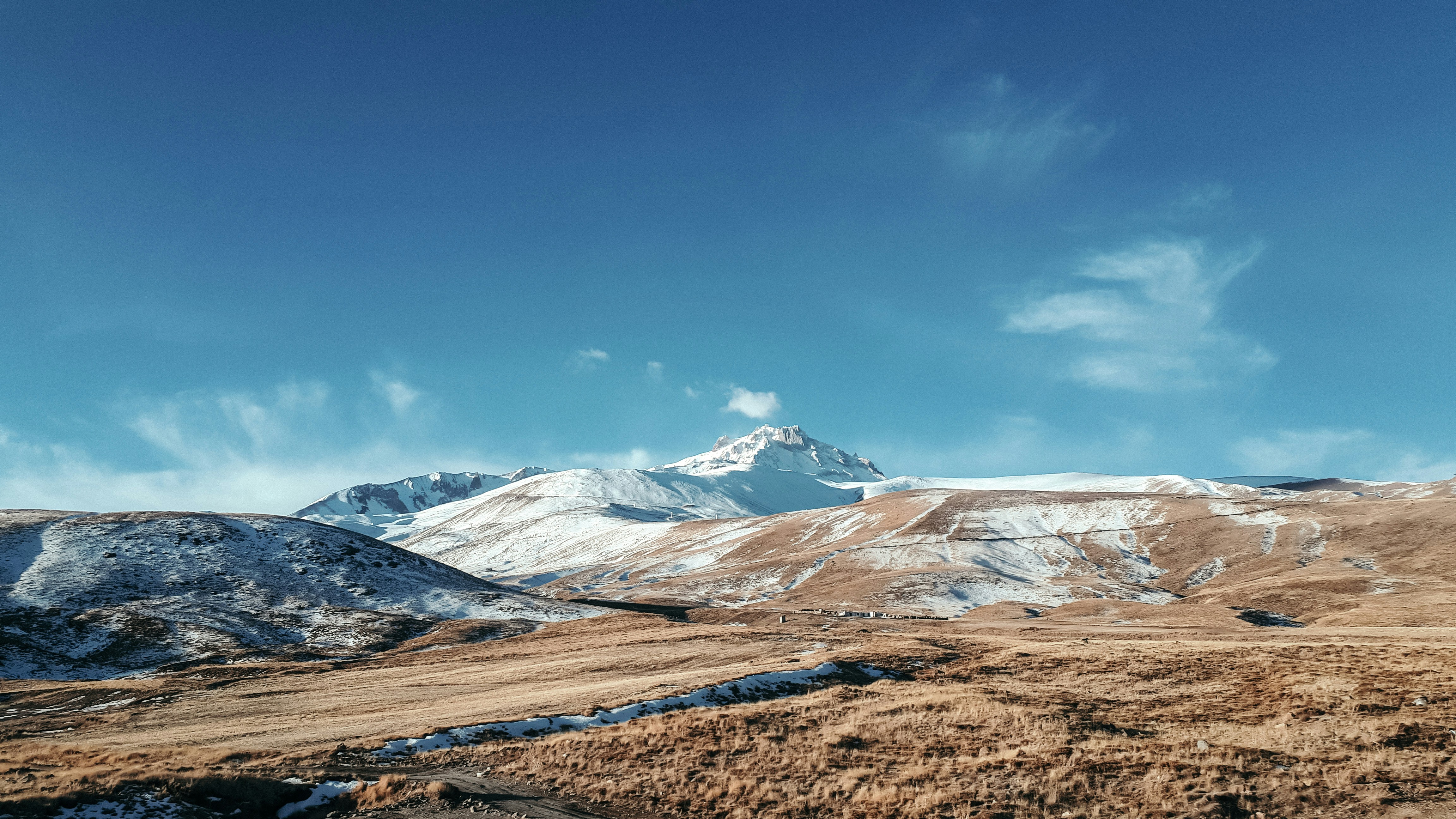 Snow-capped mountains under a clear blue sky with wispy clouds.