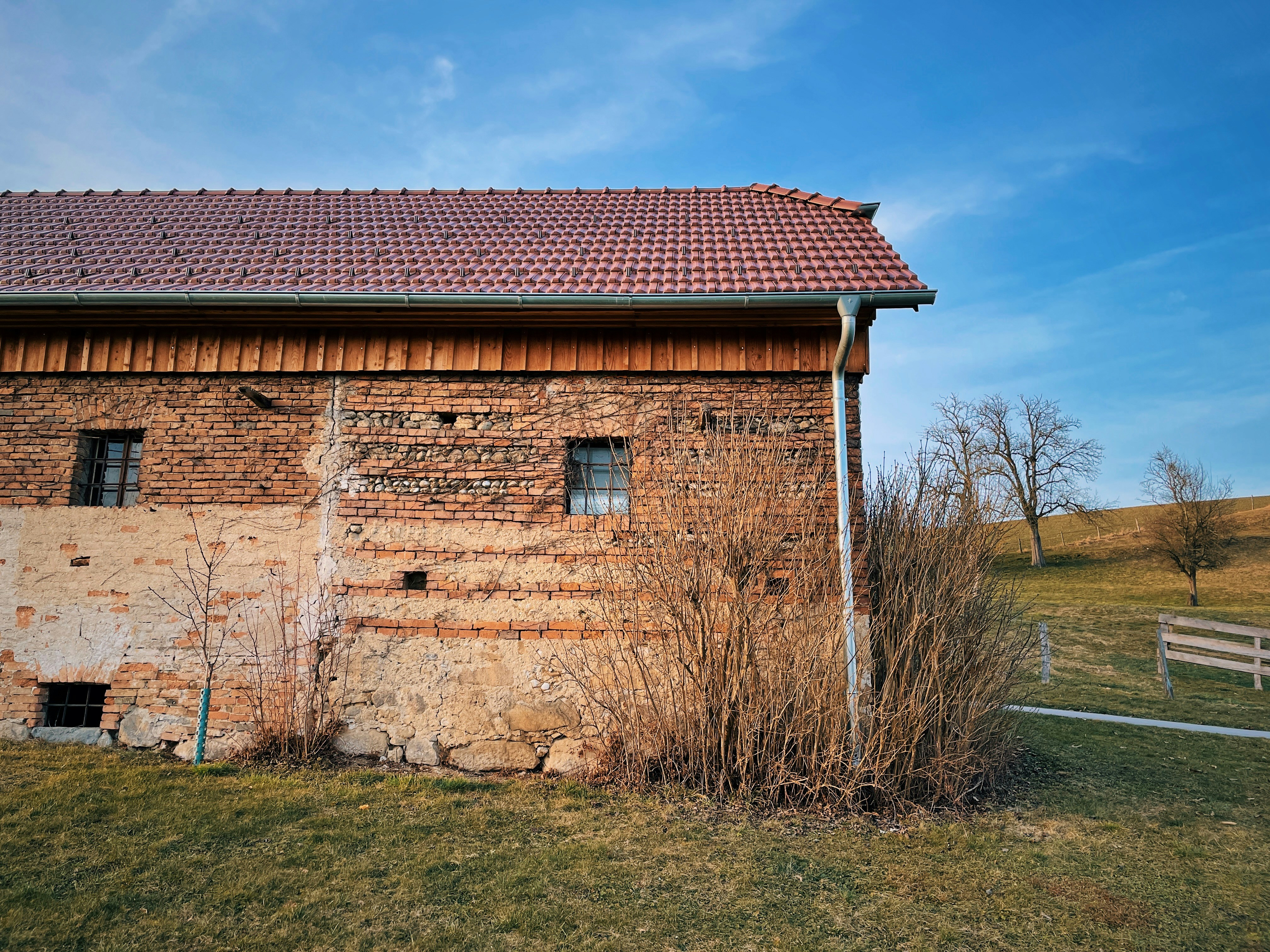 A rustic building showcasing a blend of aged bricks and wooden accents, surrounded by sparse vegetation against a clear blue sky.