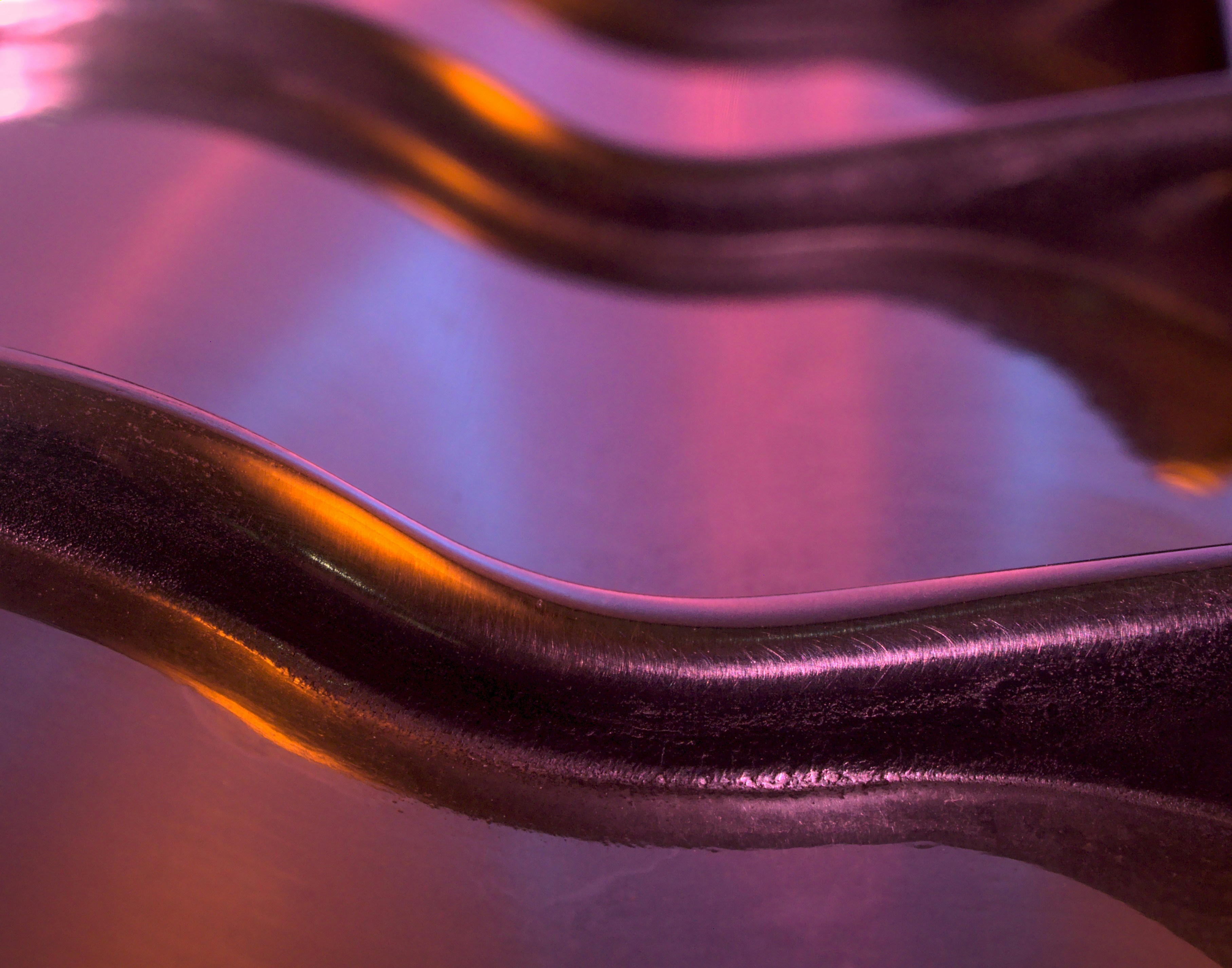 Close-up of a griddle surface with vibrant reflections of pink and orange light creating an abstract pattern.