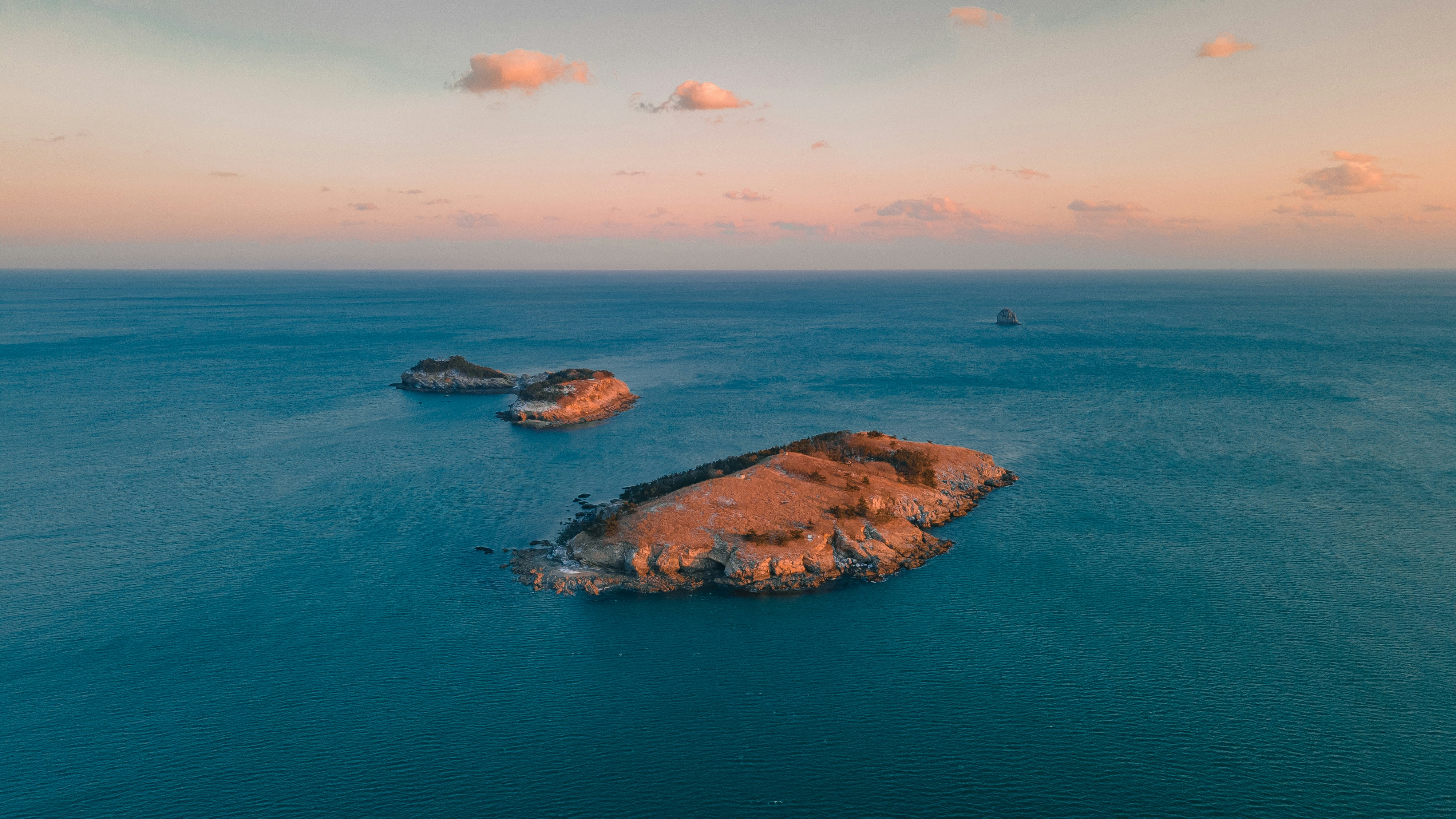 Three islands emerging from calm ocean waters during sunset, showcasing the interplay of light and shadow on the landscape.