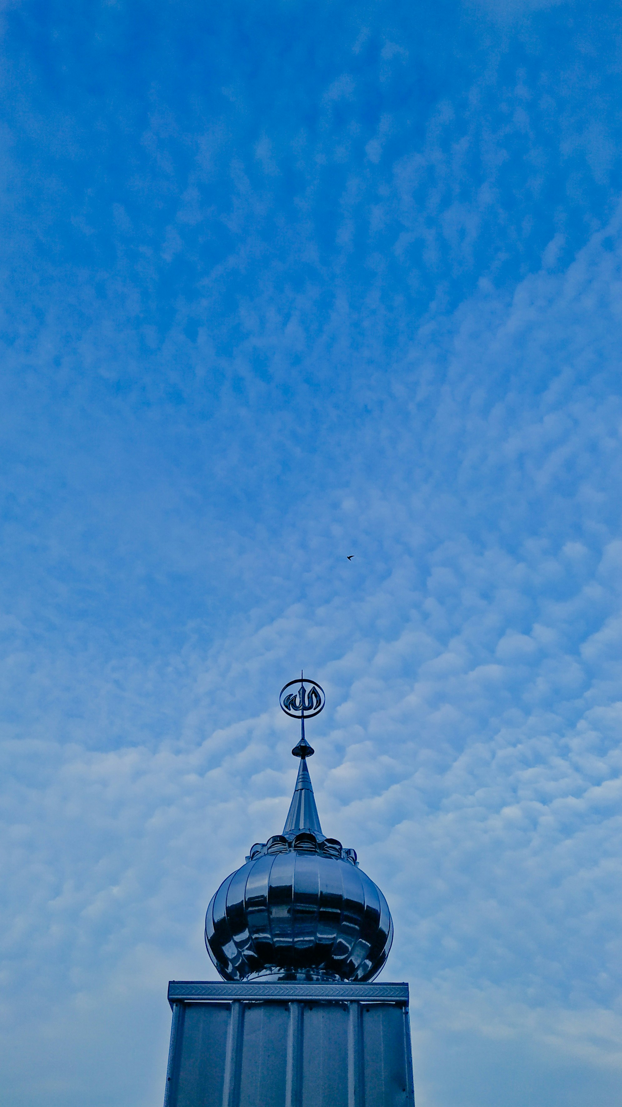Shimmering dome of a mosque reaching towards a vibrant blue sky filled with textured clouds.