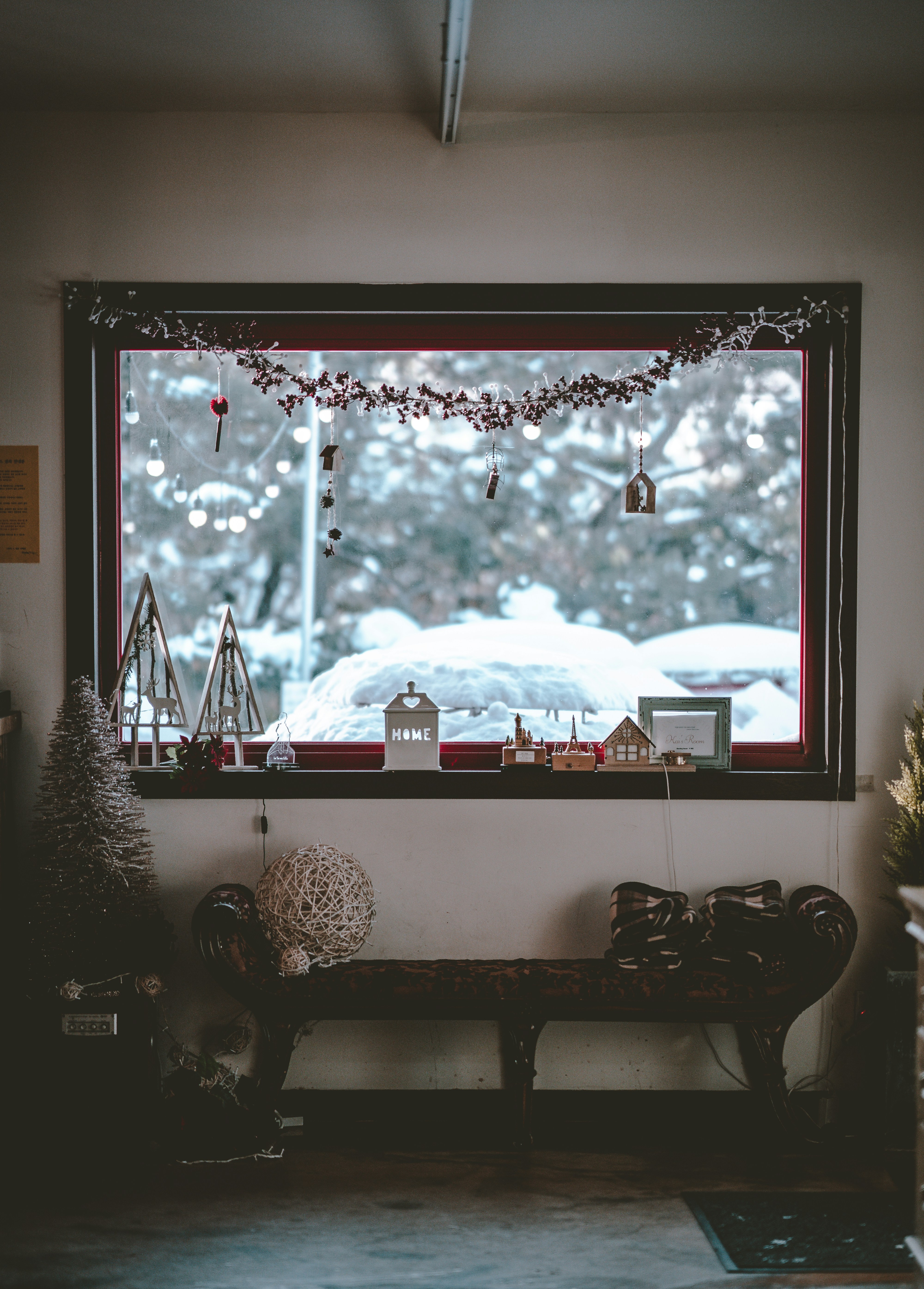 Decorative window showcasing a winter landscape with snow-covered trees and festive ornaments. The interior features a cozy bench and holiday decor.