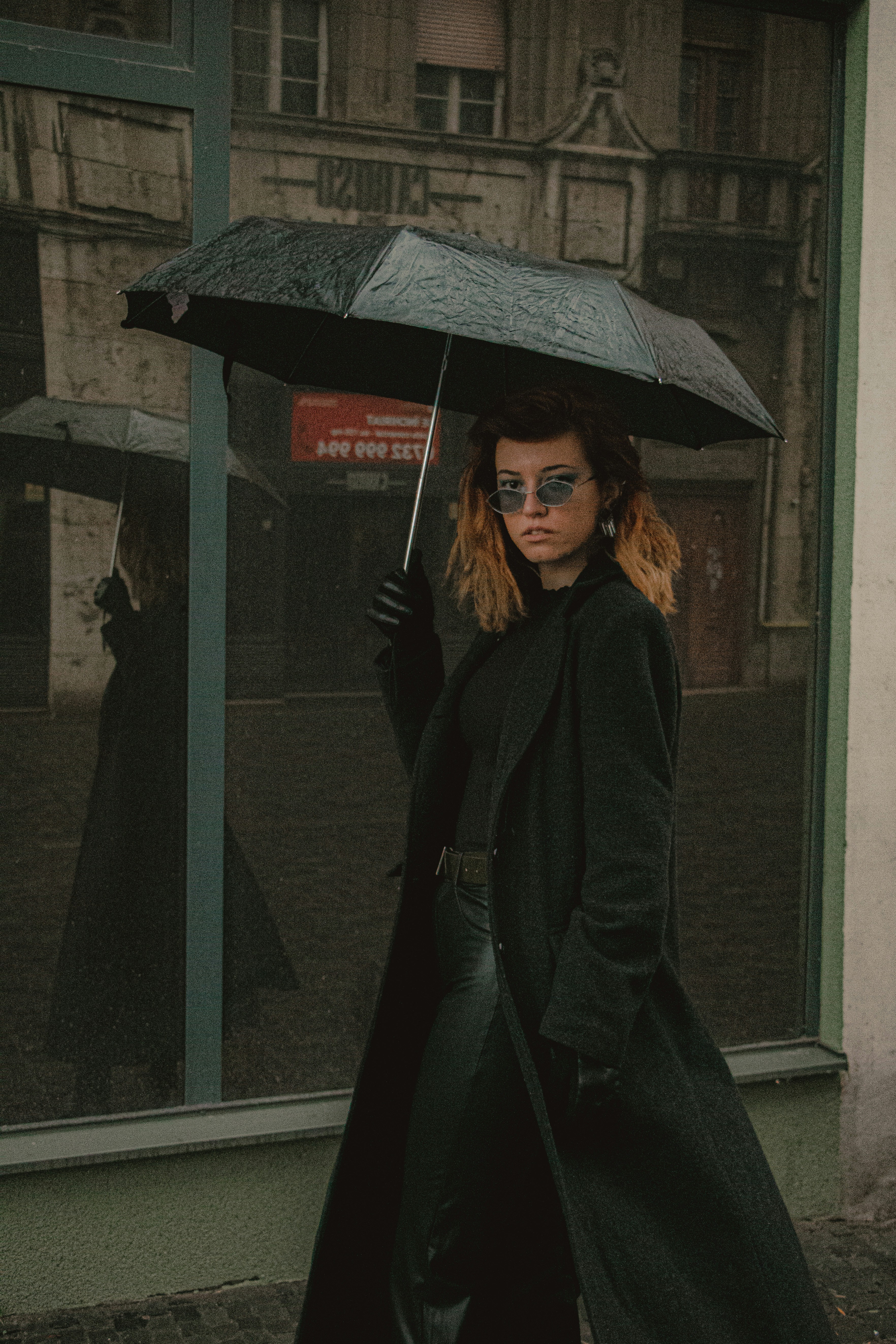 Rain-Soaked Reflections: A Street Portrait Framed by Glass and Umbrella