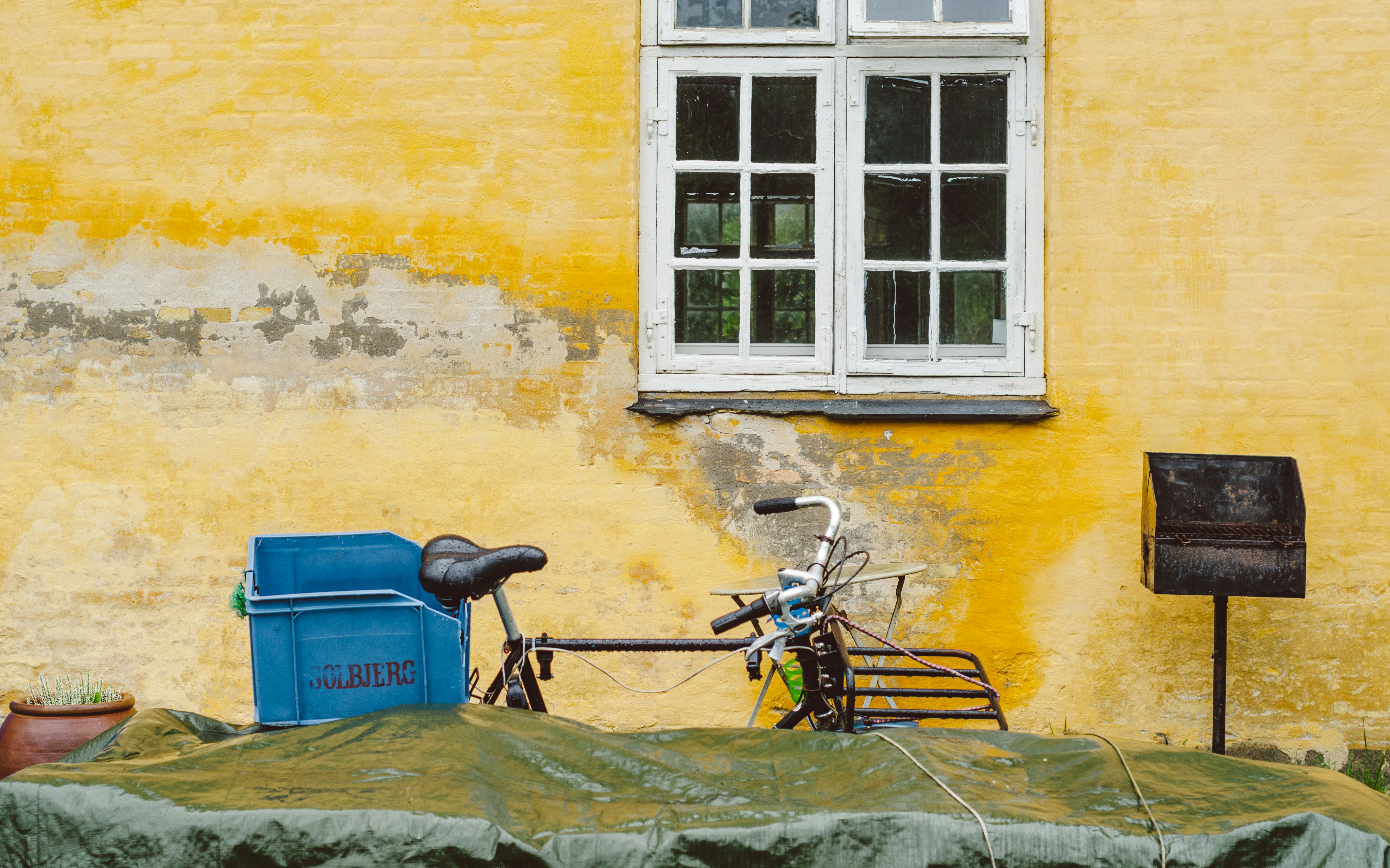 Bicycle Resting Beneath a Sunlit Window on a Worn Yellow Facade