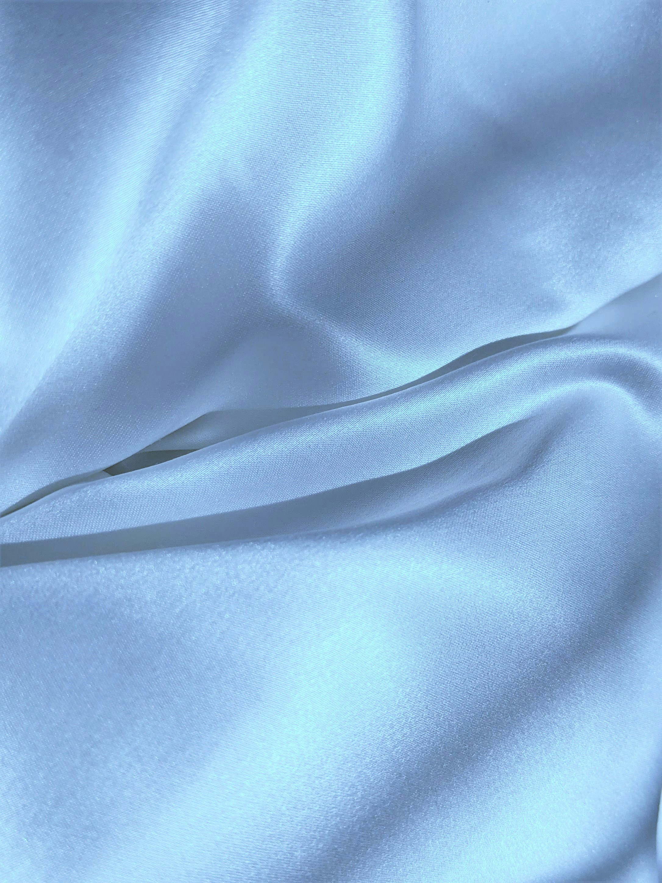 Soft blue satin fabric elegantly draped, showcasing gentle folds and reflections. The texture invites a sense of calm and luxury.