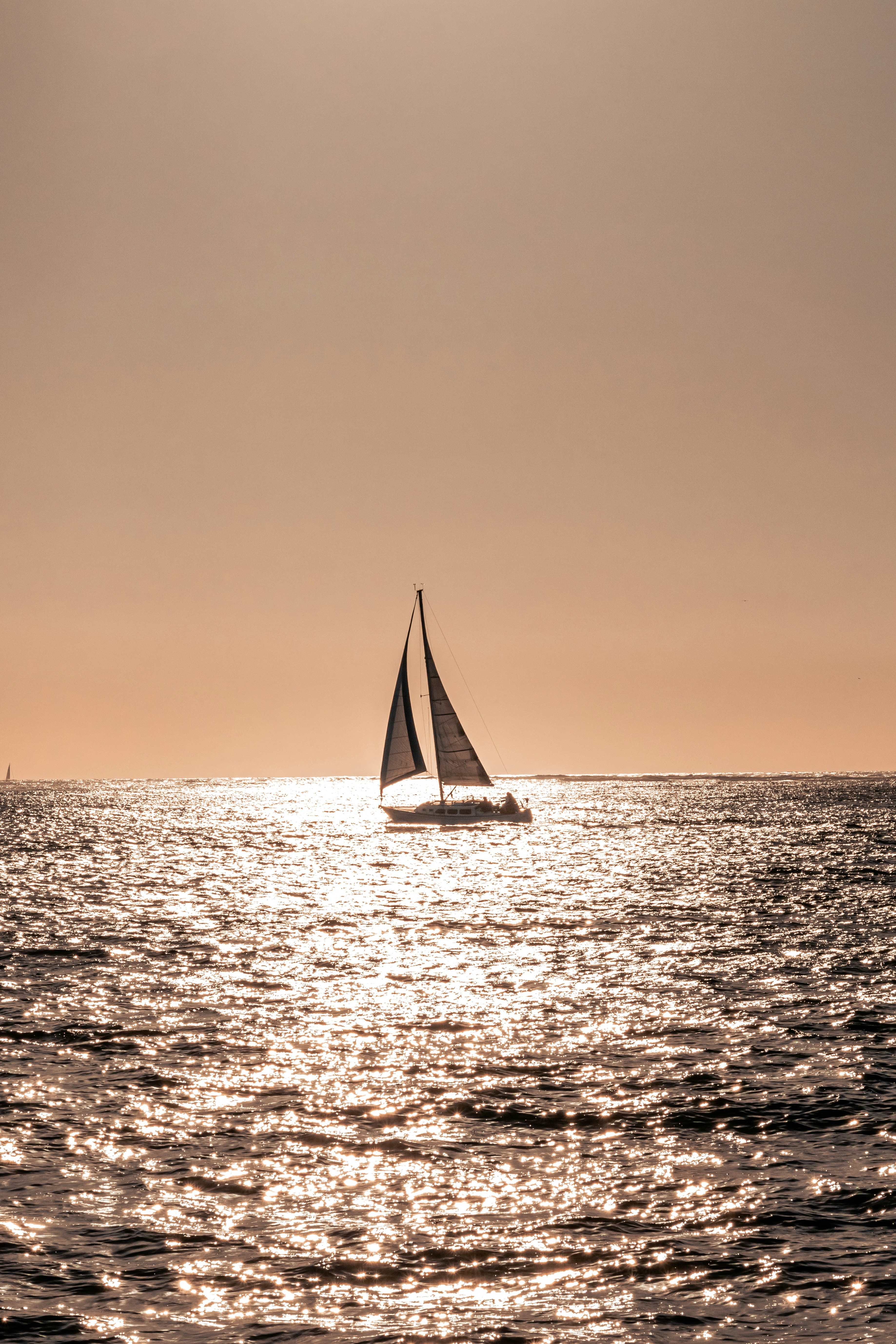 Sailboat gliding across shimmering waters at sunset, with gentle waves reflecting the warm hues of the sky.