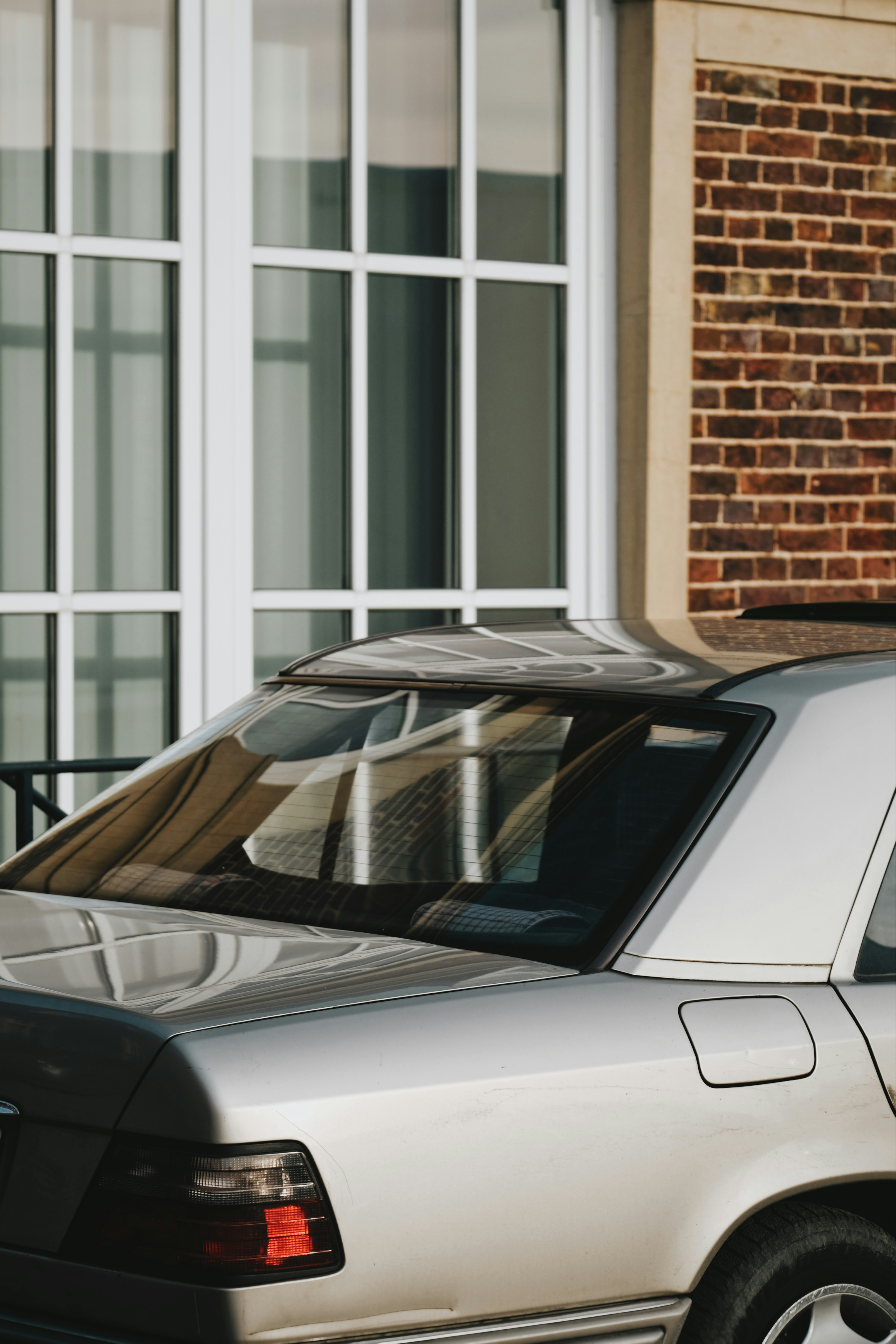 Silver Sedan by Brick Facade: Reflections on Glass and Steel