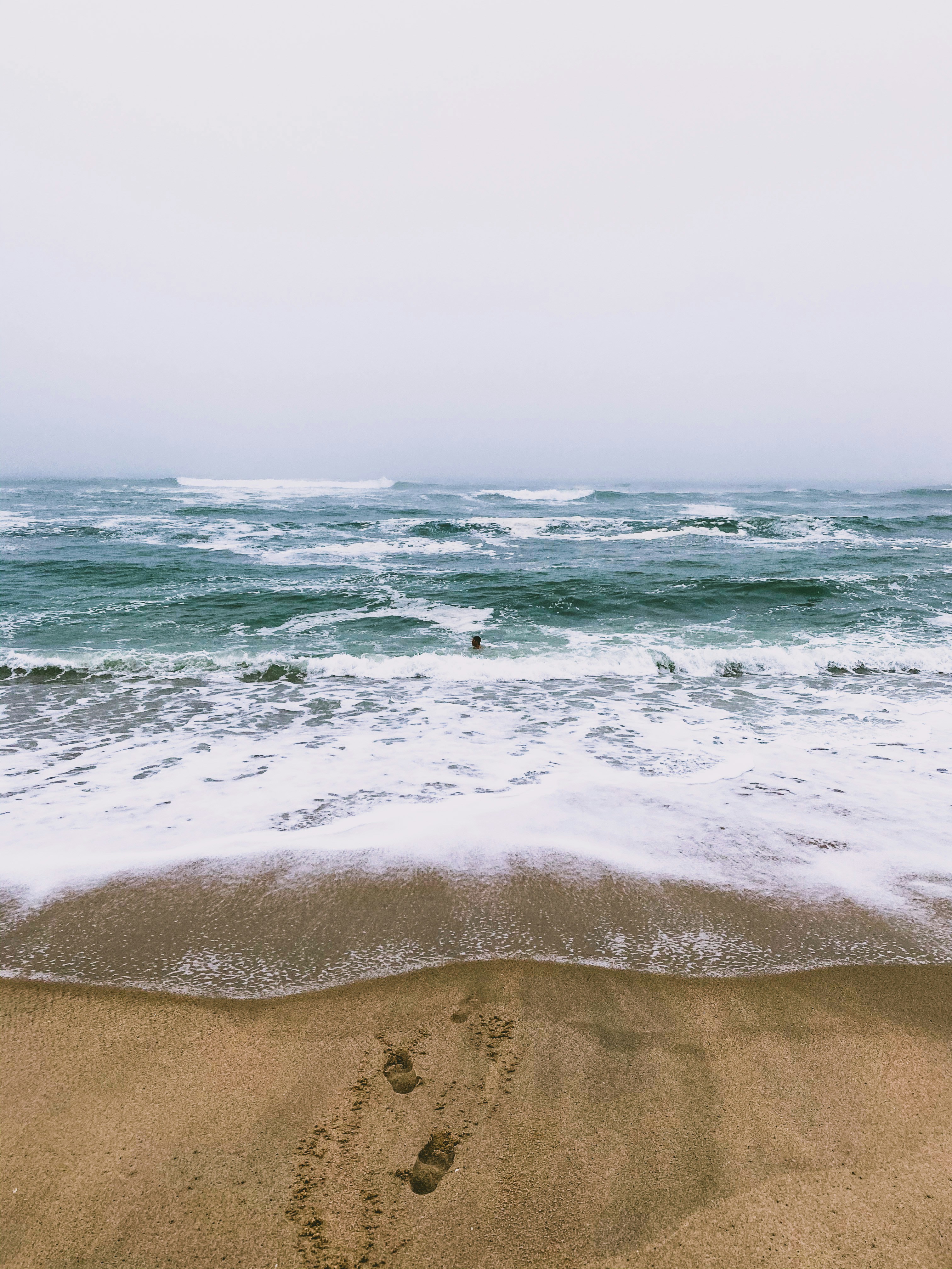Waves gently crash on a sandy beach with visible footprints leading to the water.