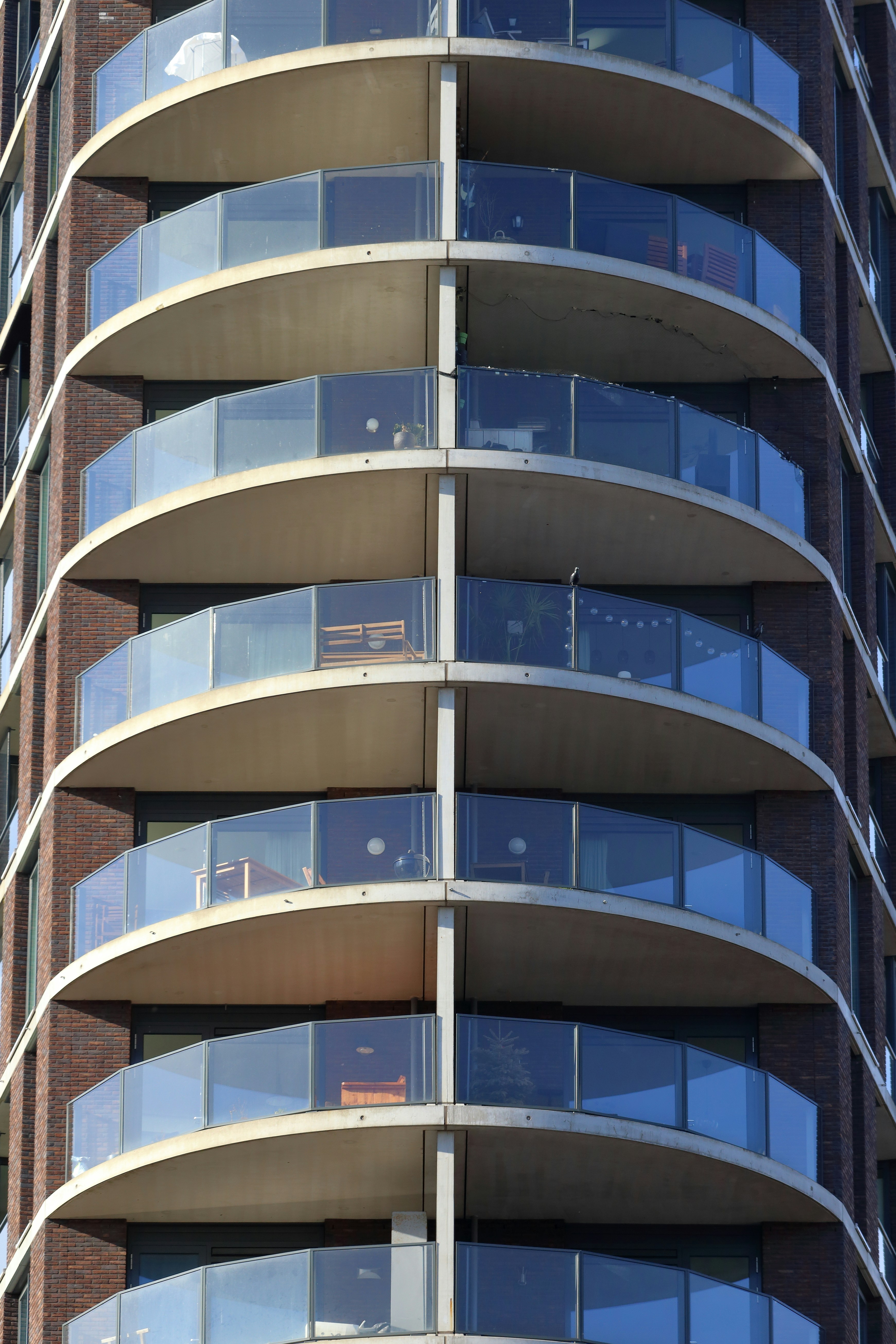 Close-up view of a modern building's balconies, showcasing their curved design and glass railings. The image highlights the architectural details and patterns.
