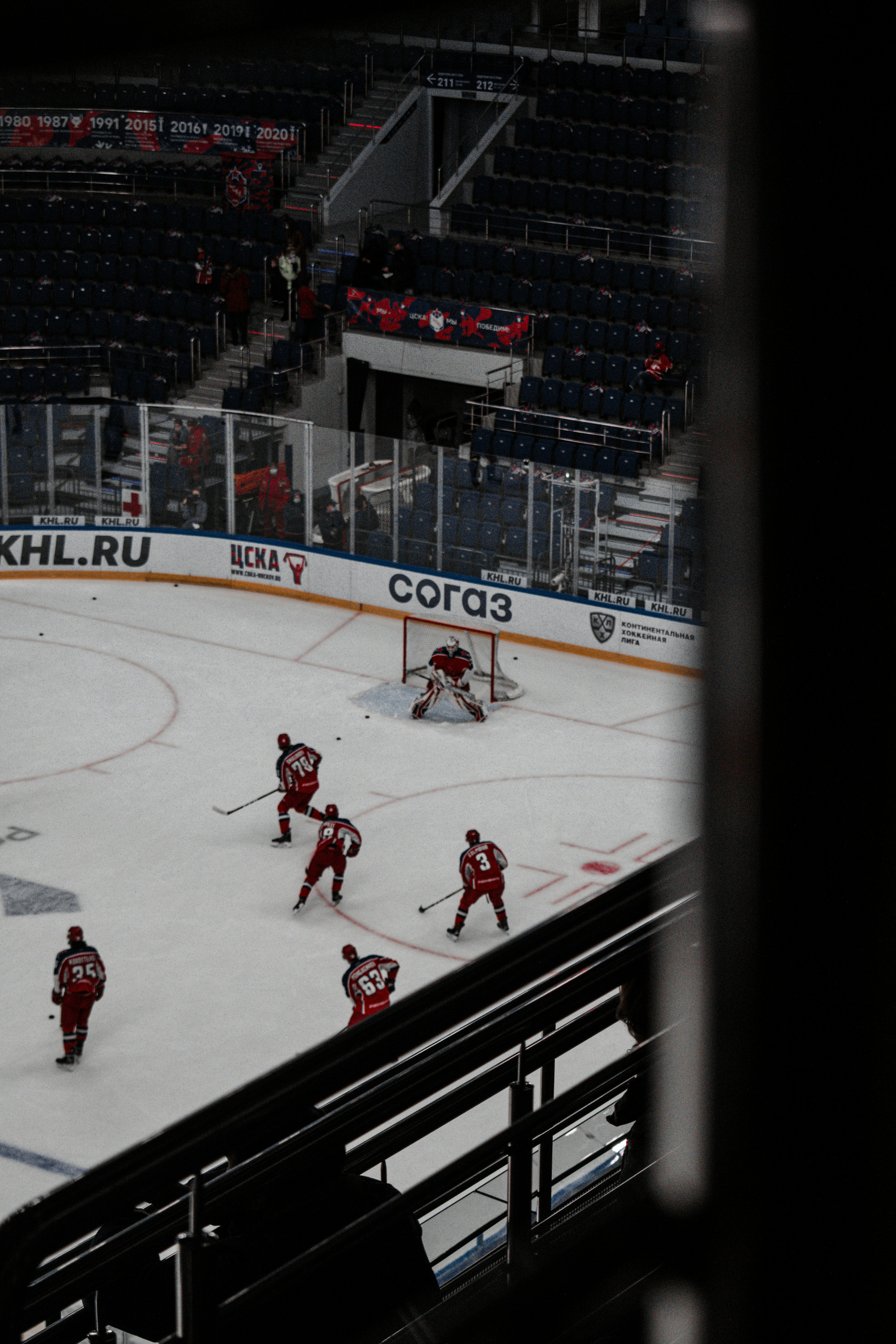 Red-clad skaters converge before the goaltender in a dimly lit rink