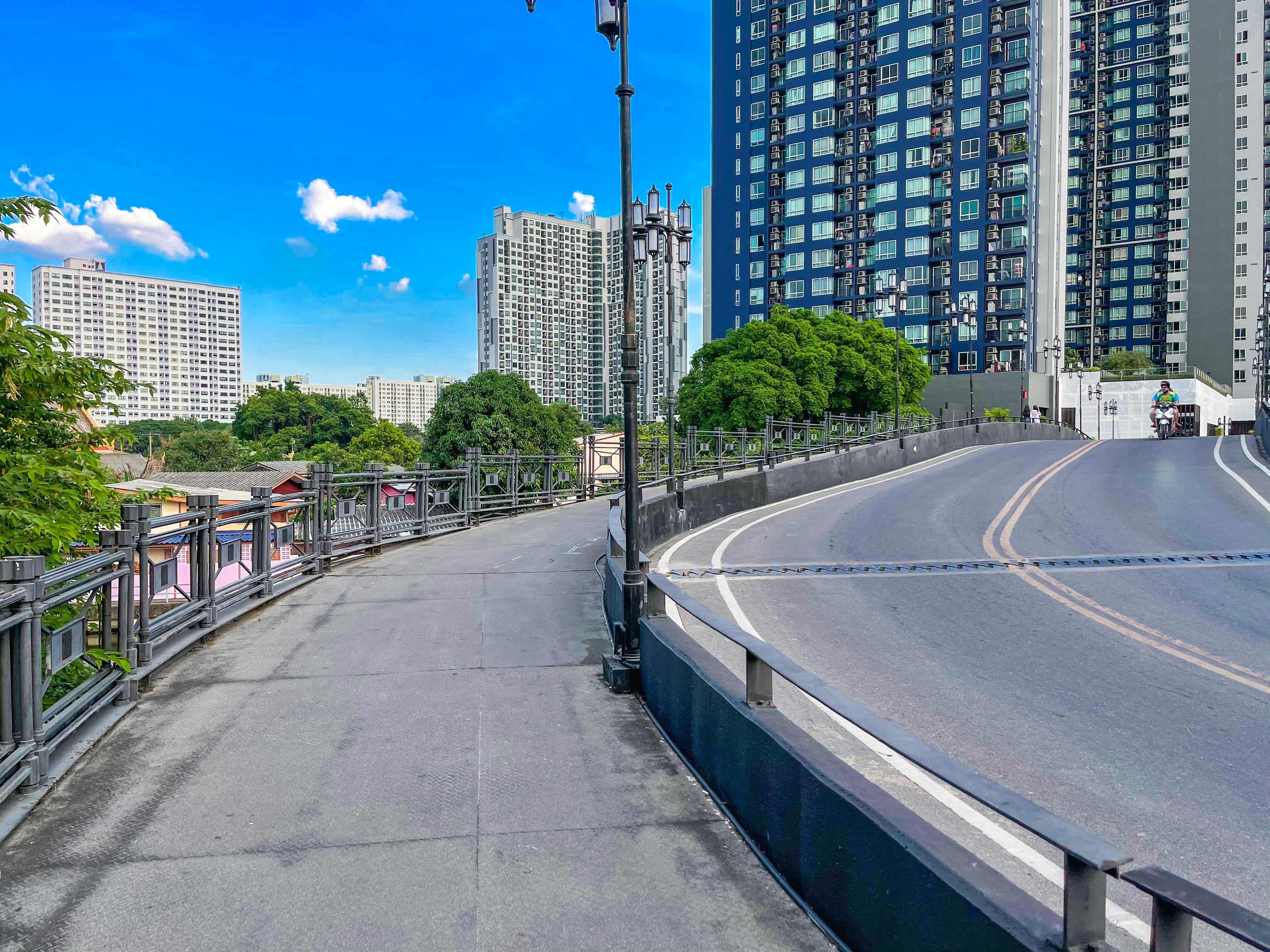 Curved urban road and pathway flanked by high-rise buildings under a bright blue sky.