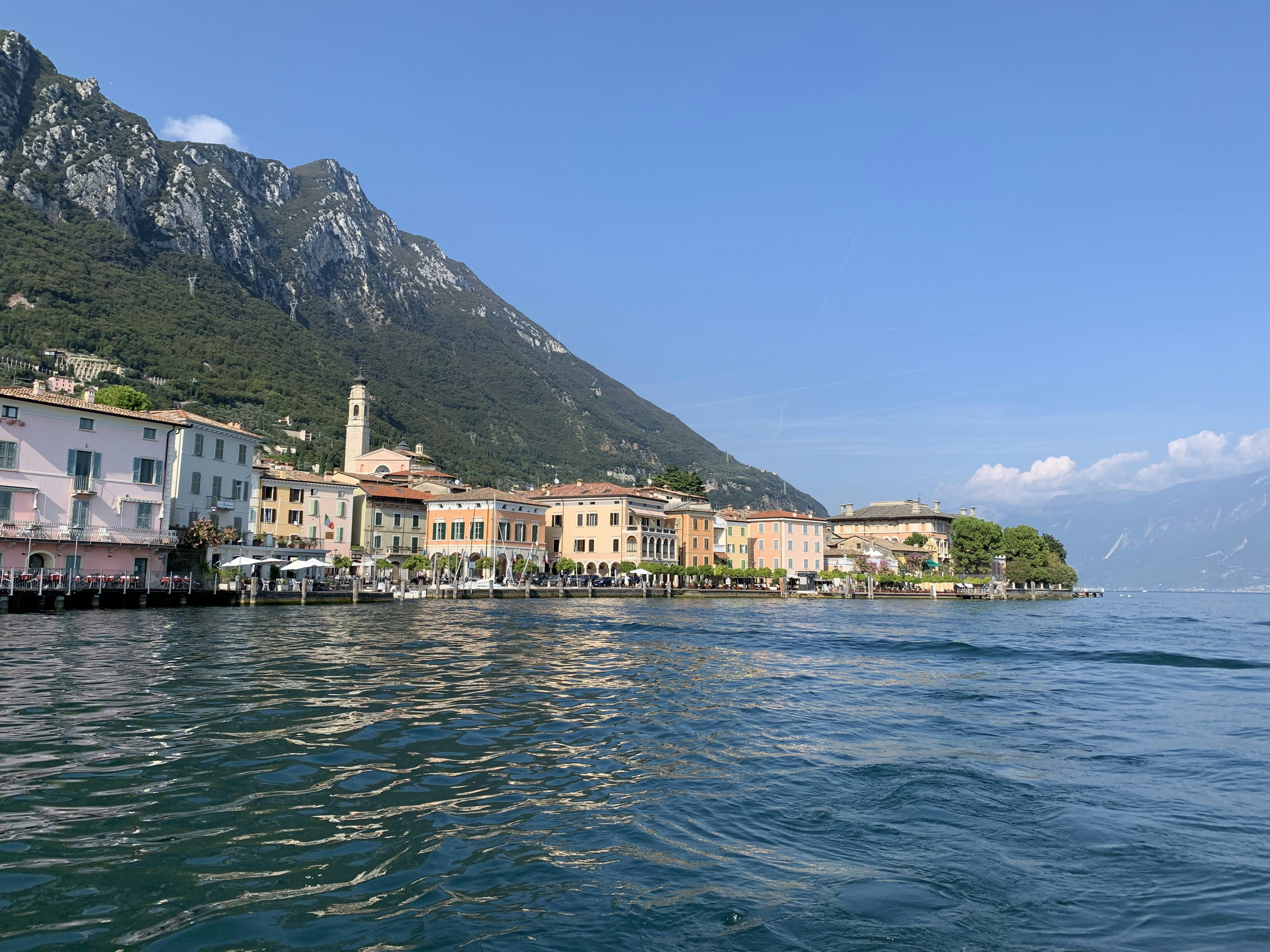 Colorful buildings line a tranquil lake with mountains in the background under a clear blue sky.