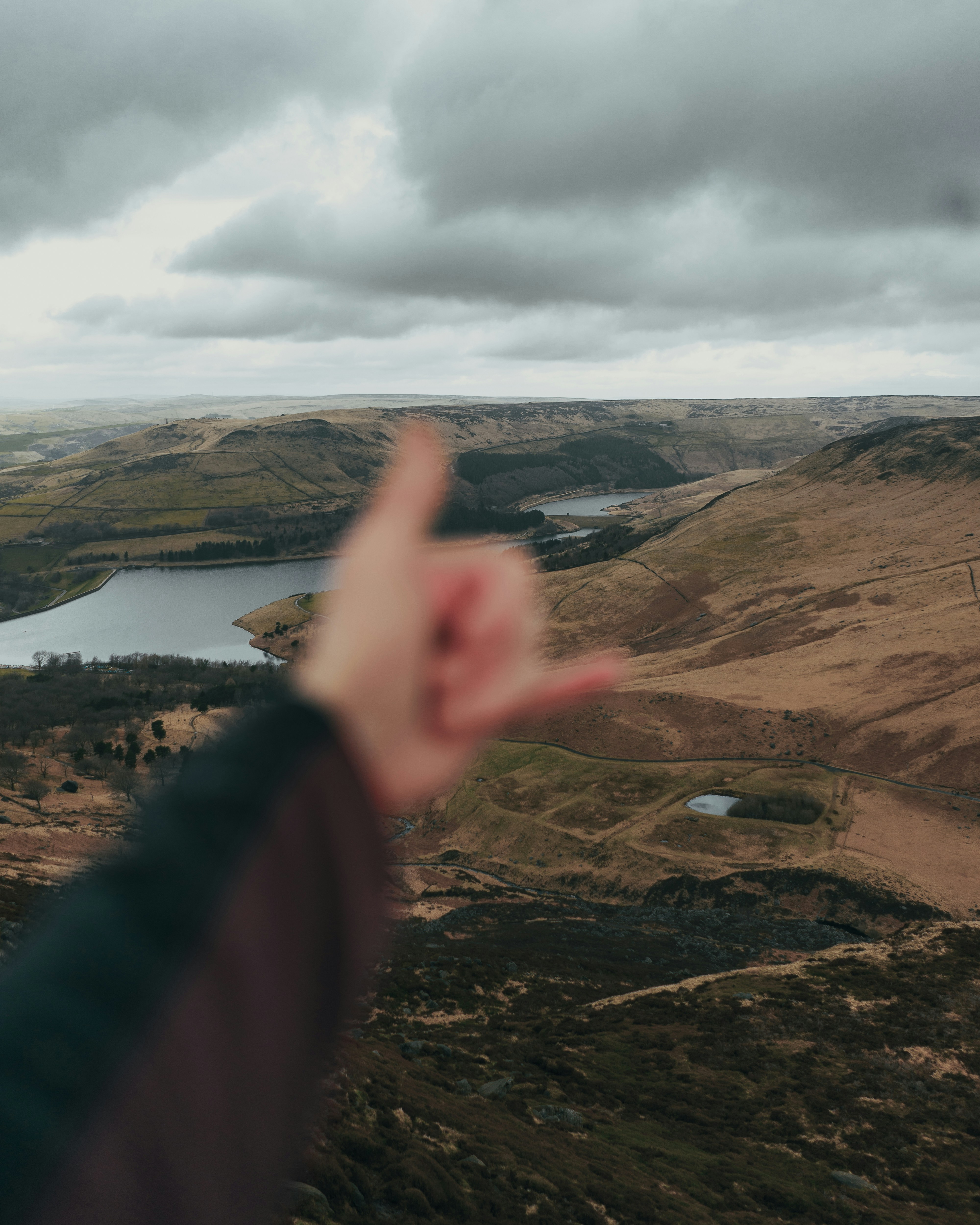 Gesture at the Horizon: A Blurred Foreground Hand Framing Moorland and Lake